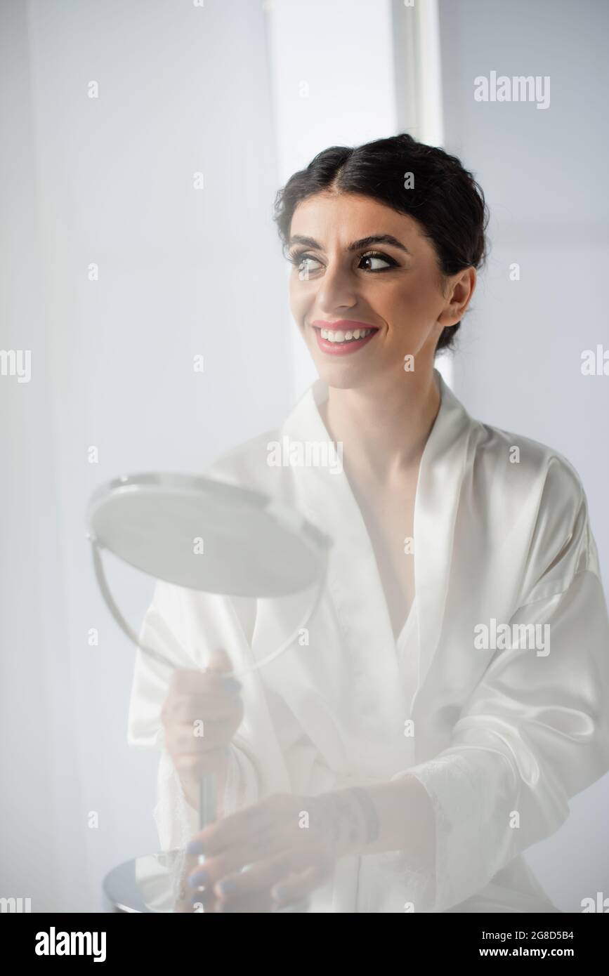 young and happy indian bride holding blurred mirror isolated on white ...