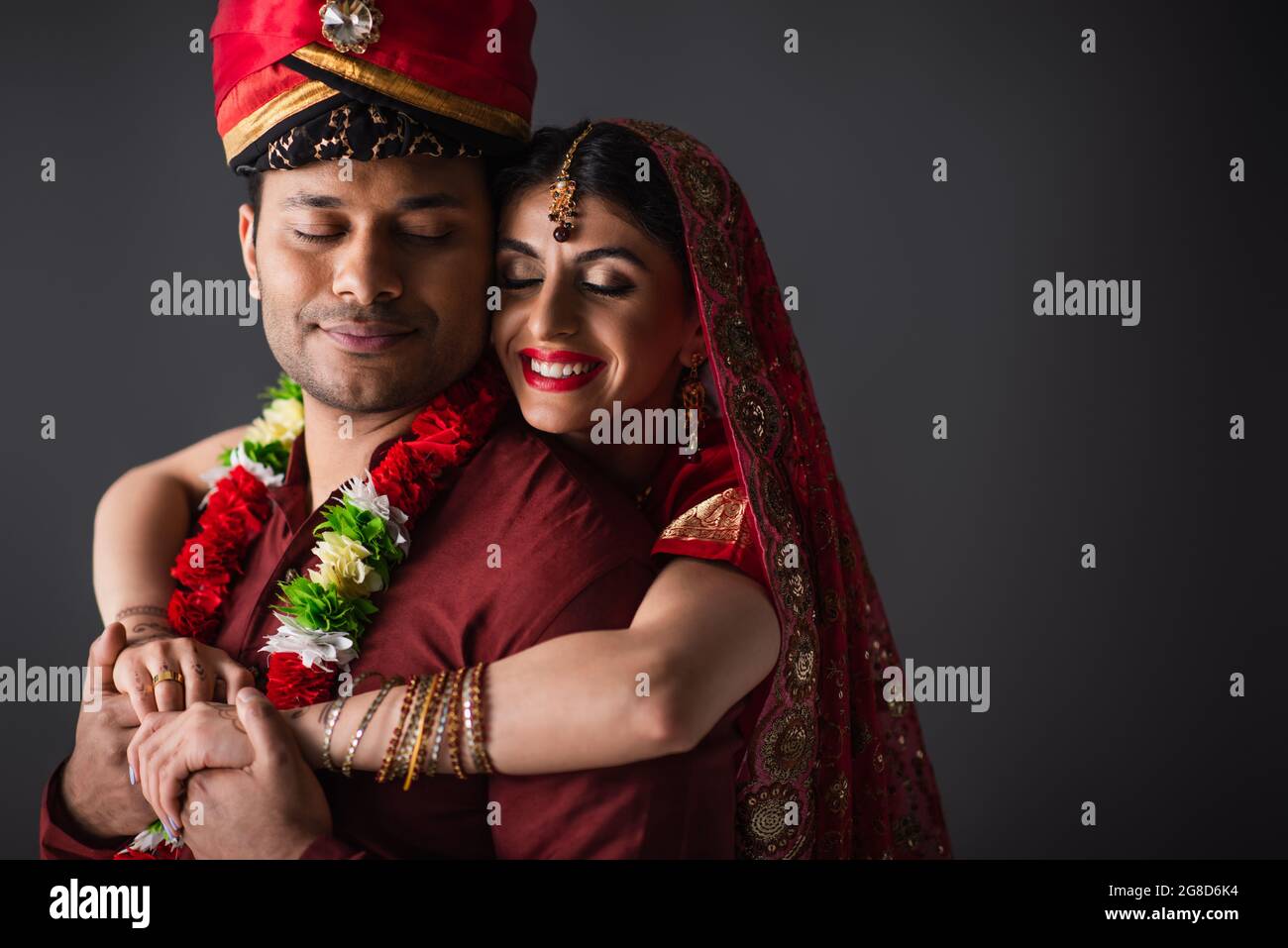 cheerful indian bride in sari hugging bridegroom in turban isolated on ...