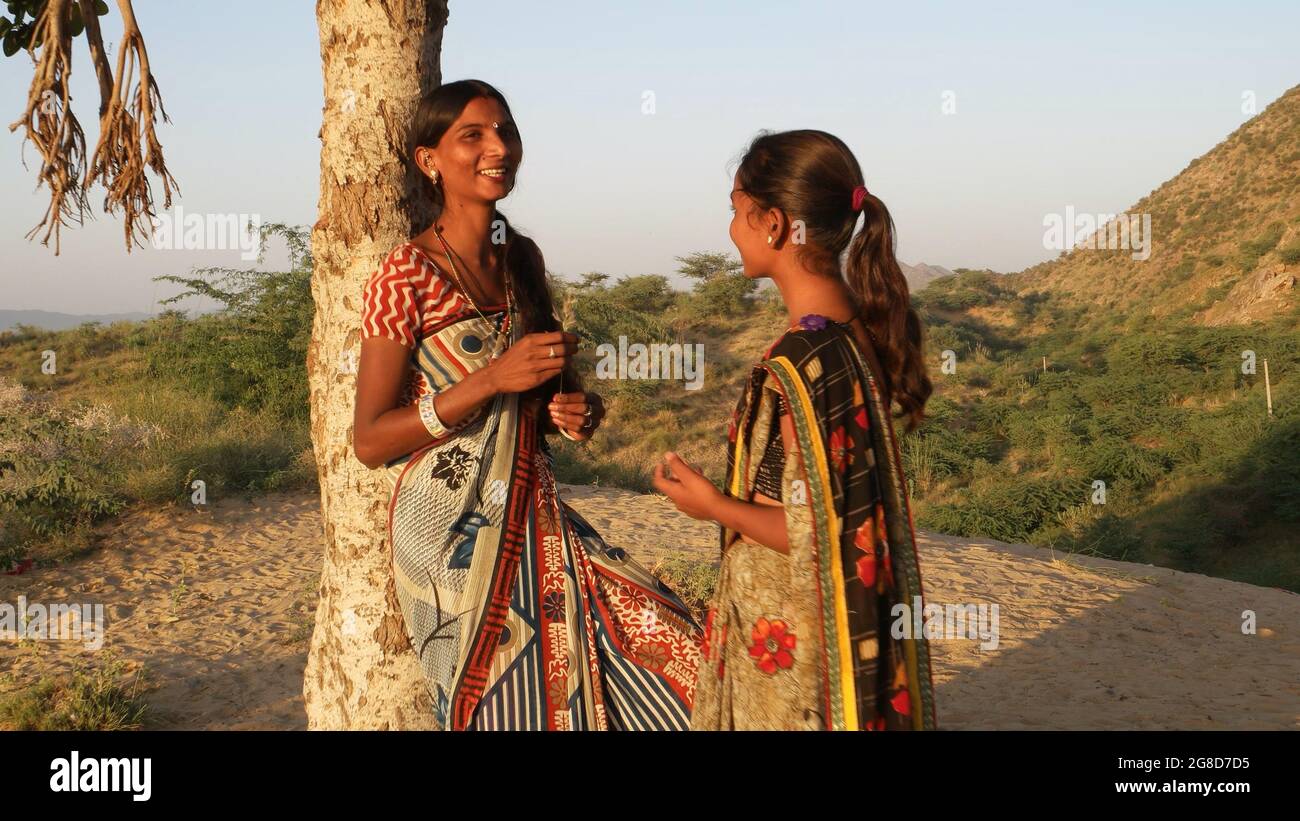 Two young Indian females standing by the tree and talking to each other ...