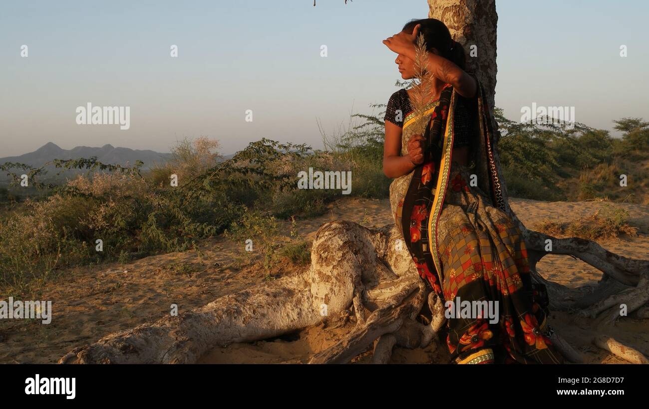 Young Indian female covering eyes from sunlights with a hand sitting on ...