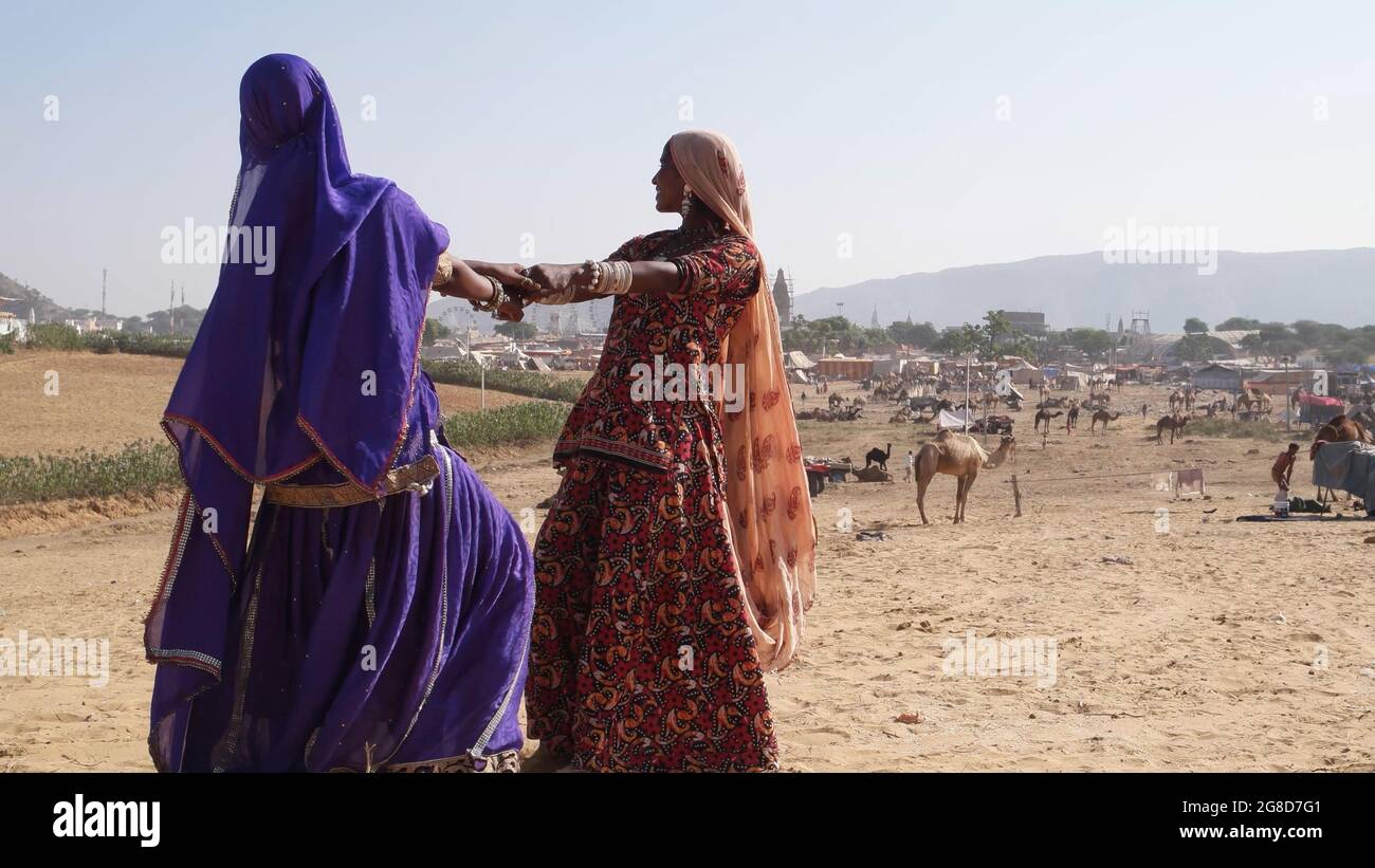 Two Indian females with colorful kerchiefs dancing in a desert under a ...