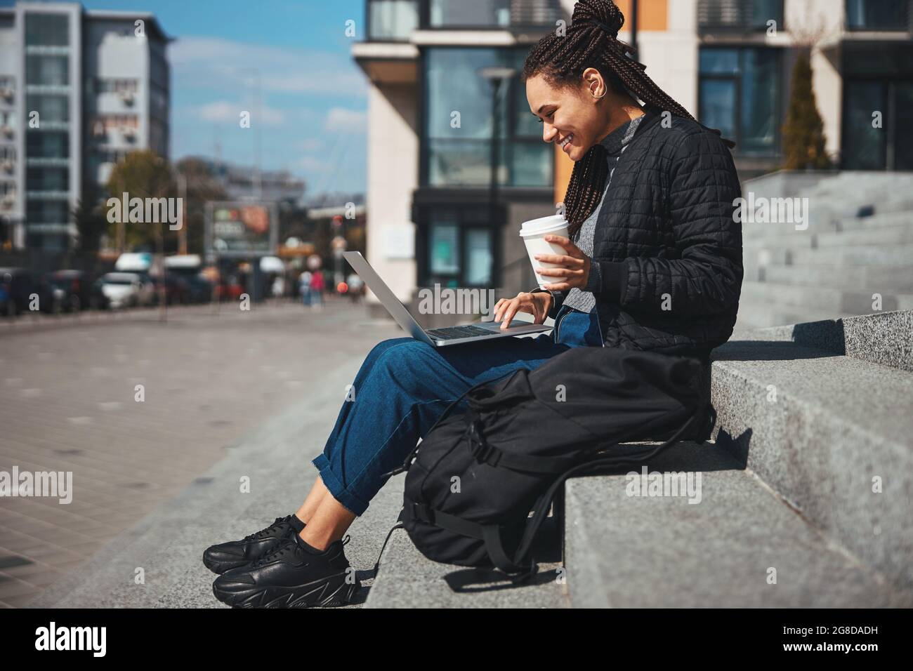 Joyful lady seated on the concrete steps using her computer Stock Photo ...