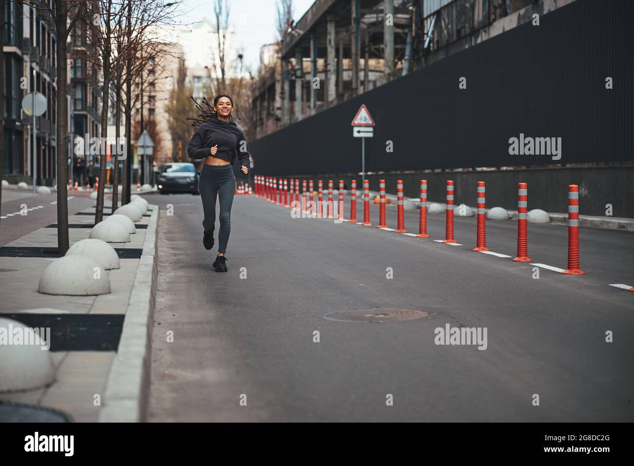 Cheerful female jogger with cornrows running ahead Stock Photo - Alamy