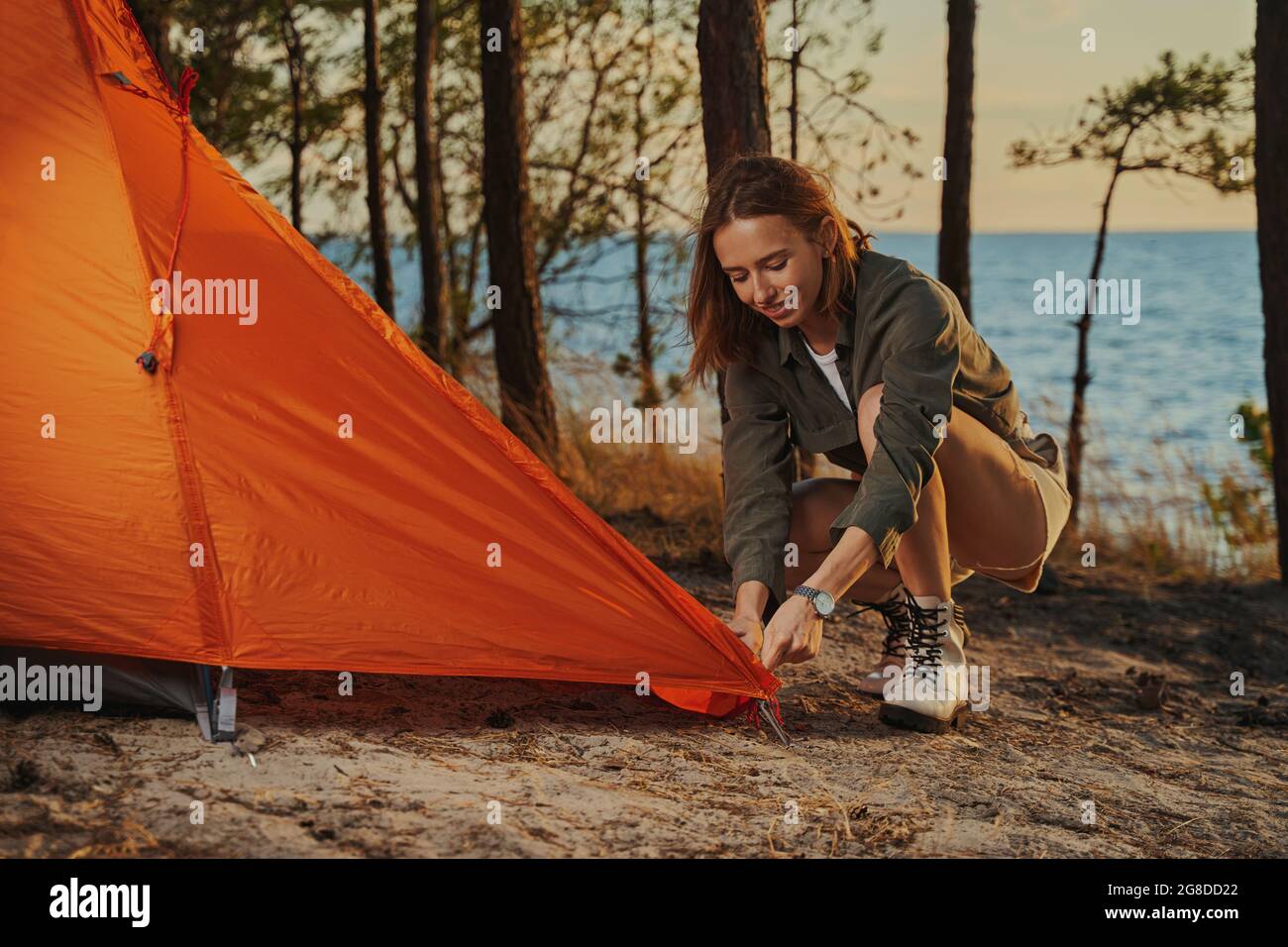 Lively woman installing an orange tent in the woods Stock Photo - Alamy