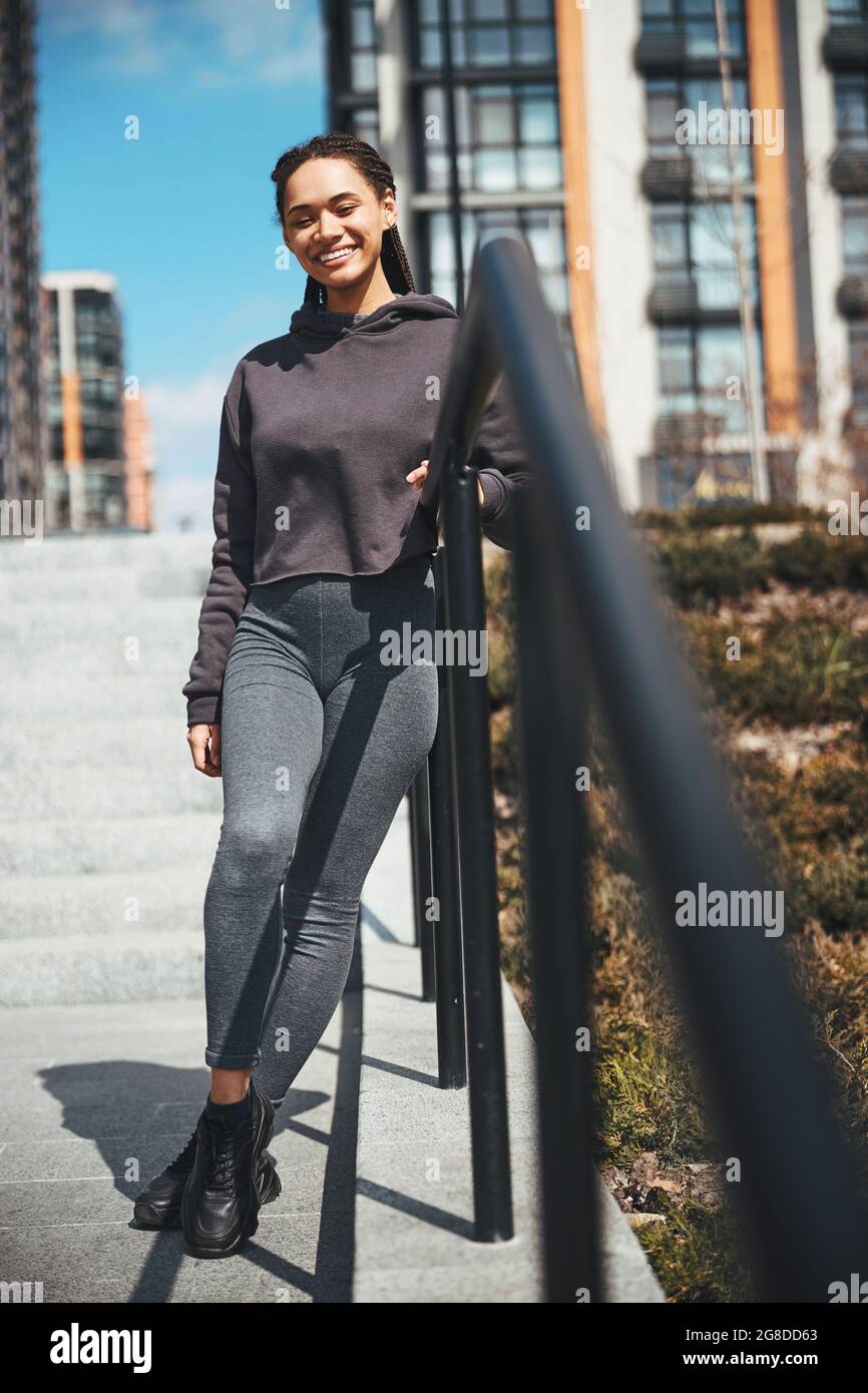 Cute athletic woman standing cross-legged on the concrete staircase ...