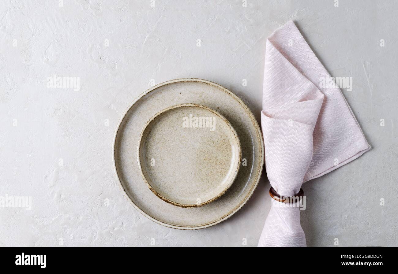 Beige ceramic plates and a pink napkin on a beige stone table. Top view ...