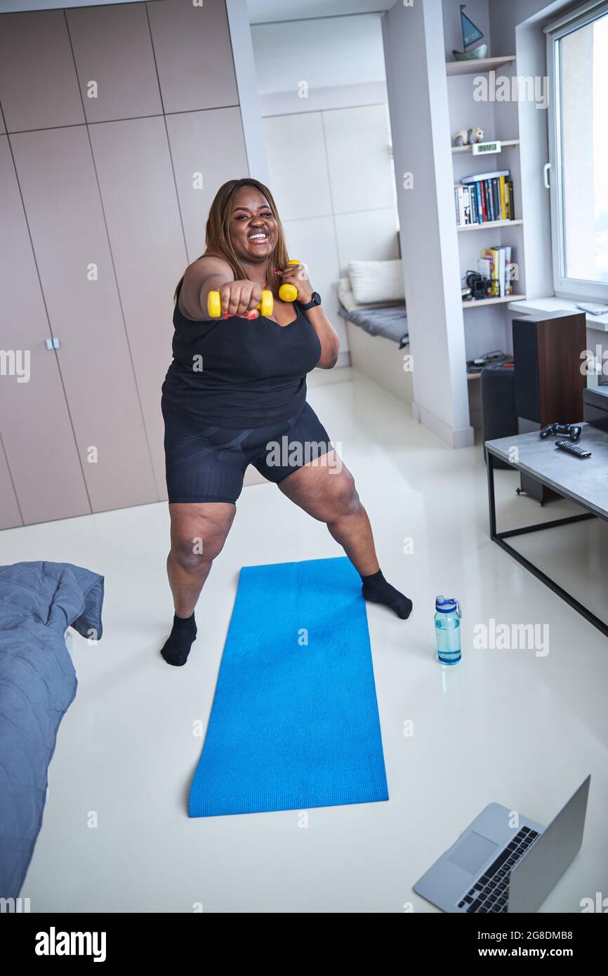 Enthusiastic African American lady exercising with dumbbells Stock ...