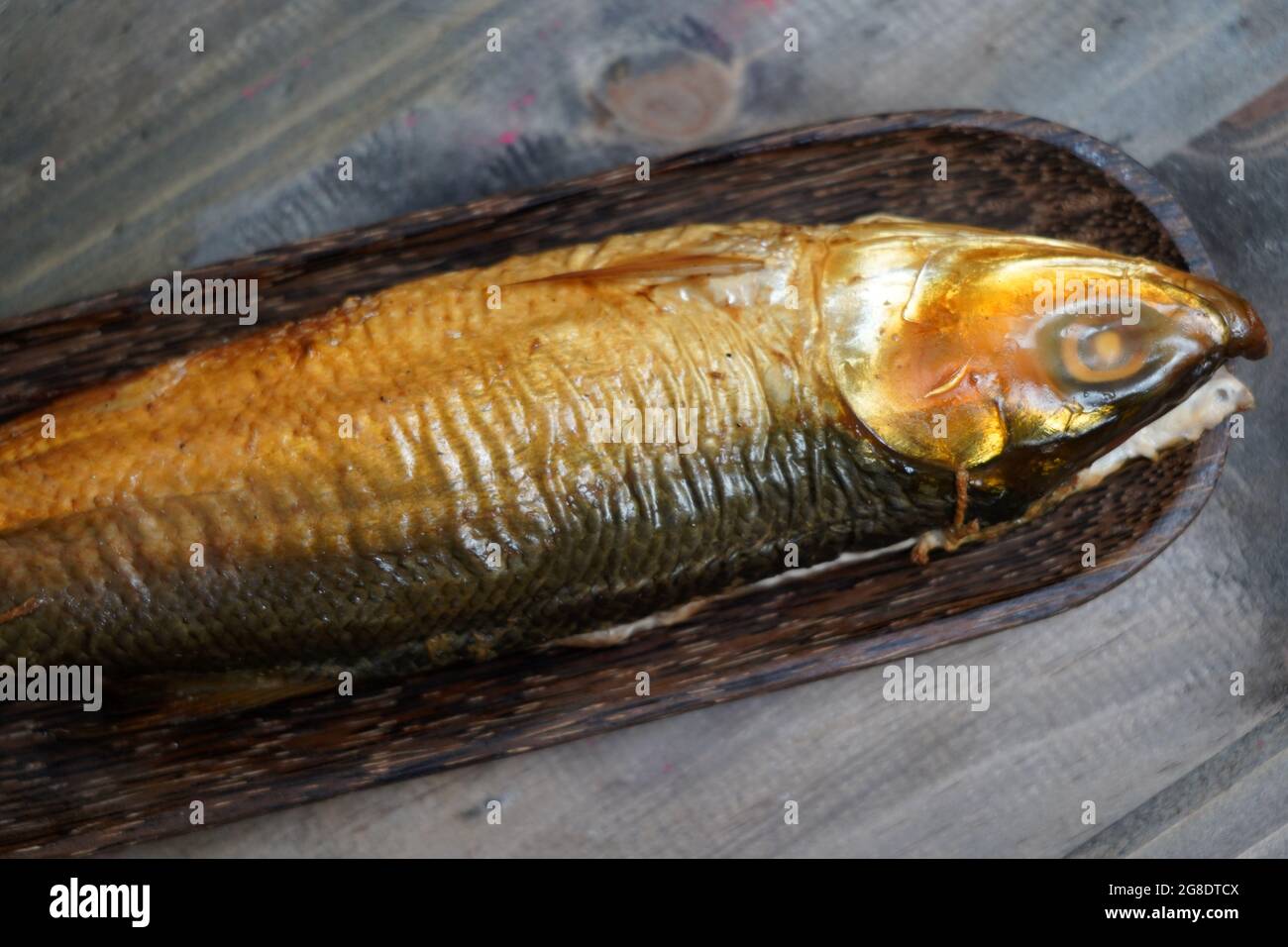 Top view of an upside-down smoked fish served in a thin long wooden ...