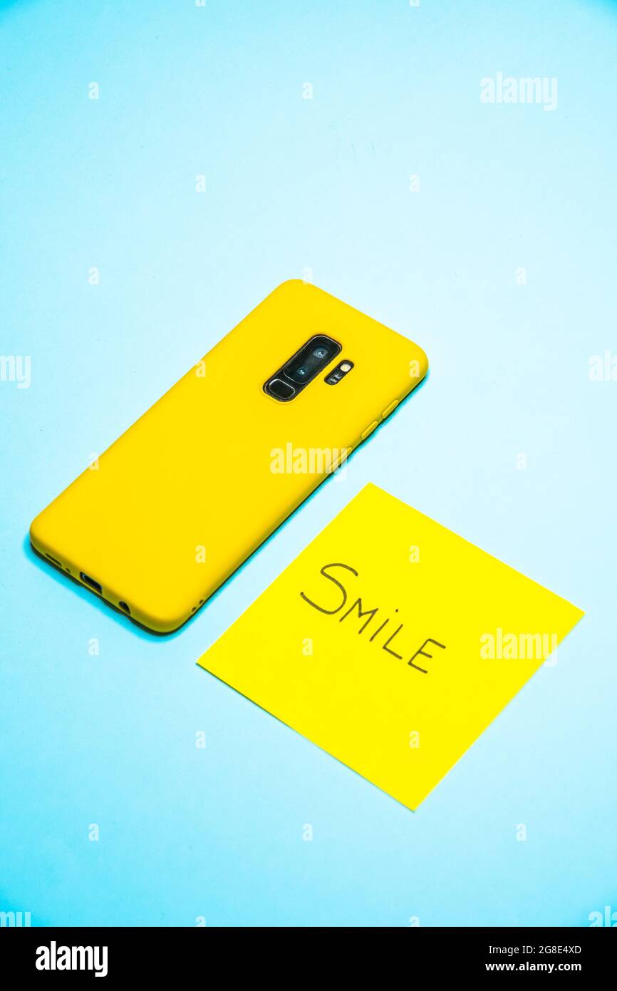 Yellow phone and a sticky note with the word Smile on a bright blue ...