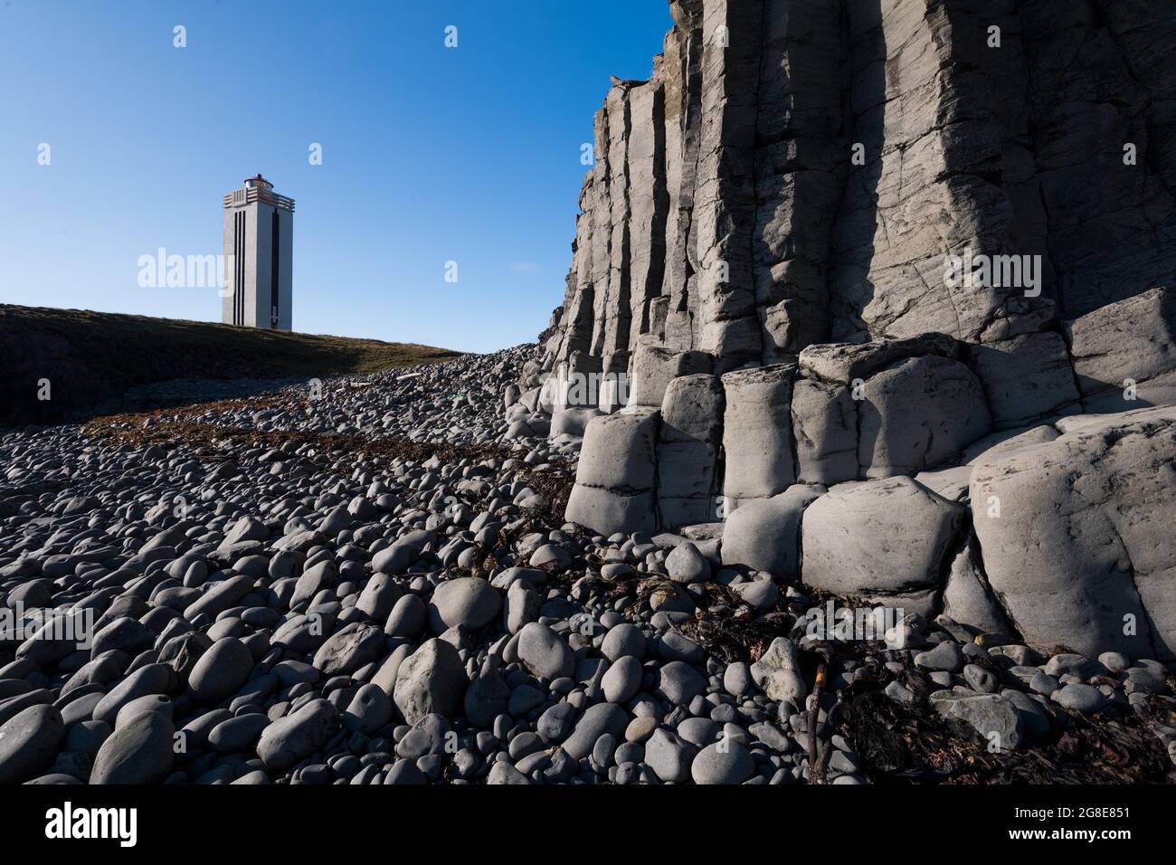 Basalt cliff, beach with rounded stones and lighthouse, Kalfshamarsvik ...