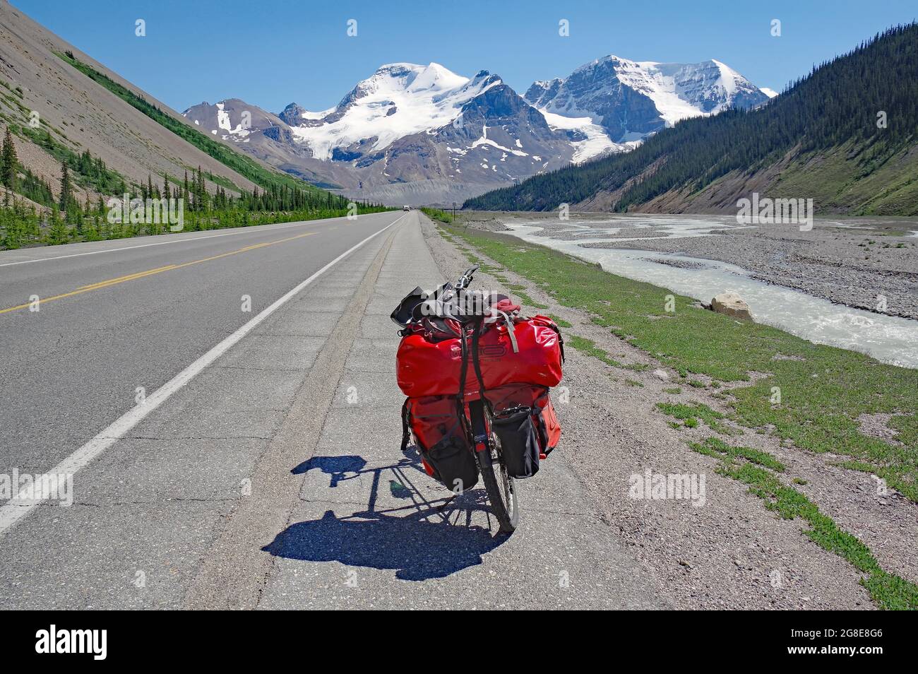 Loaded red touring bike on straight road, high mountains and glaciers ...