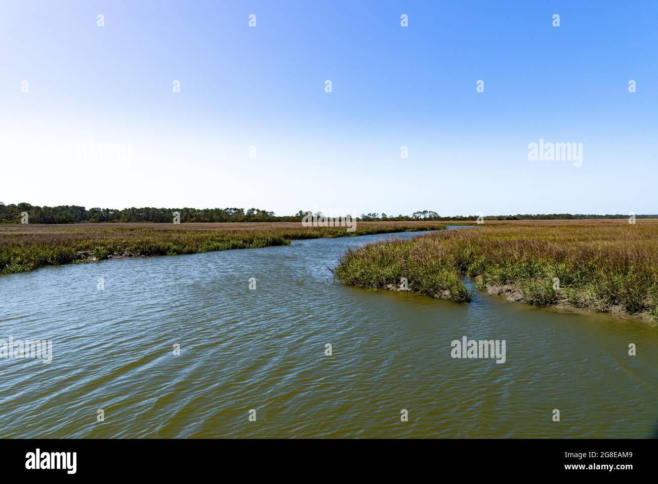Salt marsh waterway with blue sky reflected in moving tidal water ...