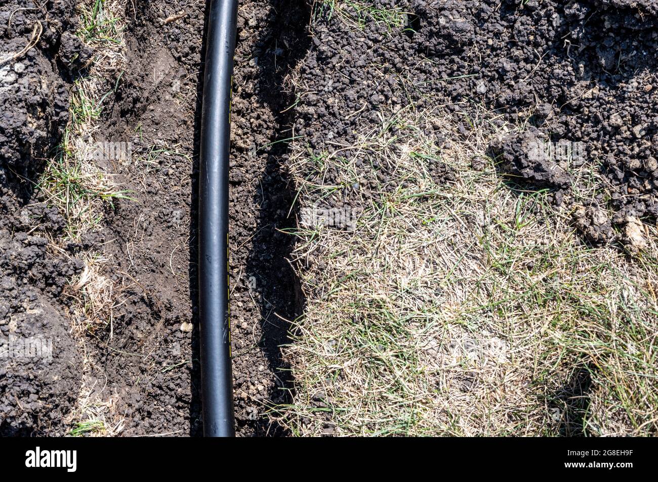 Focus on a black 1 inch sprinkler plastic water line laid in a shallow ...