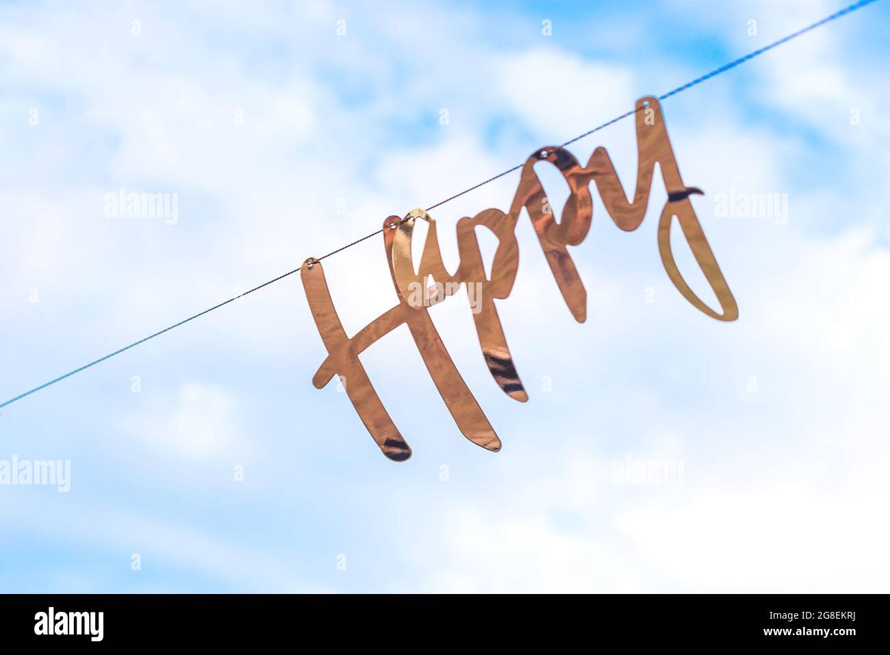 Golden word happy hangs on garland against background of blue sky with ...