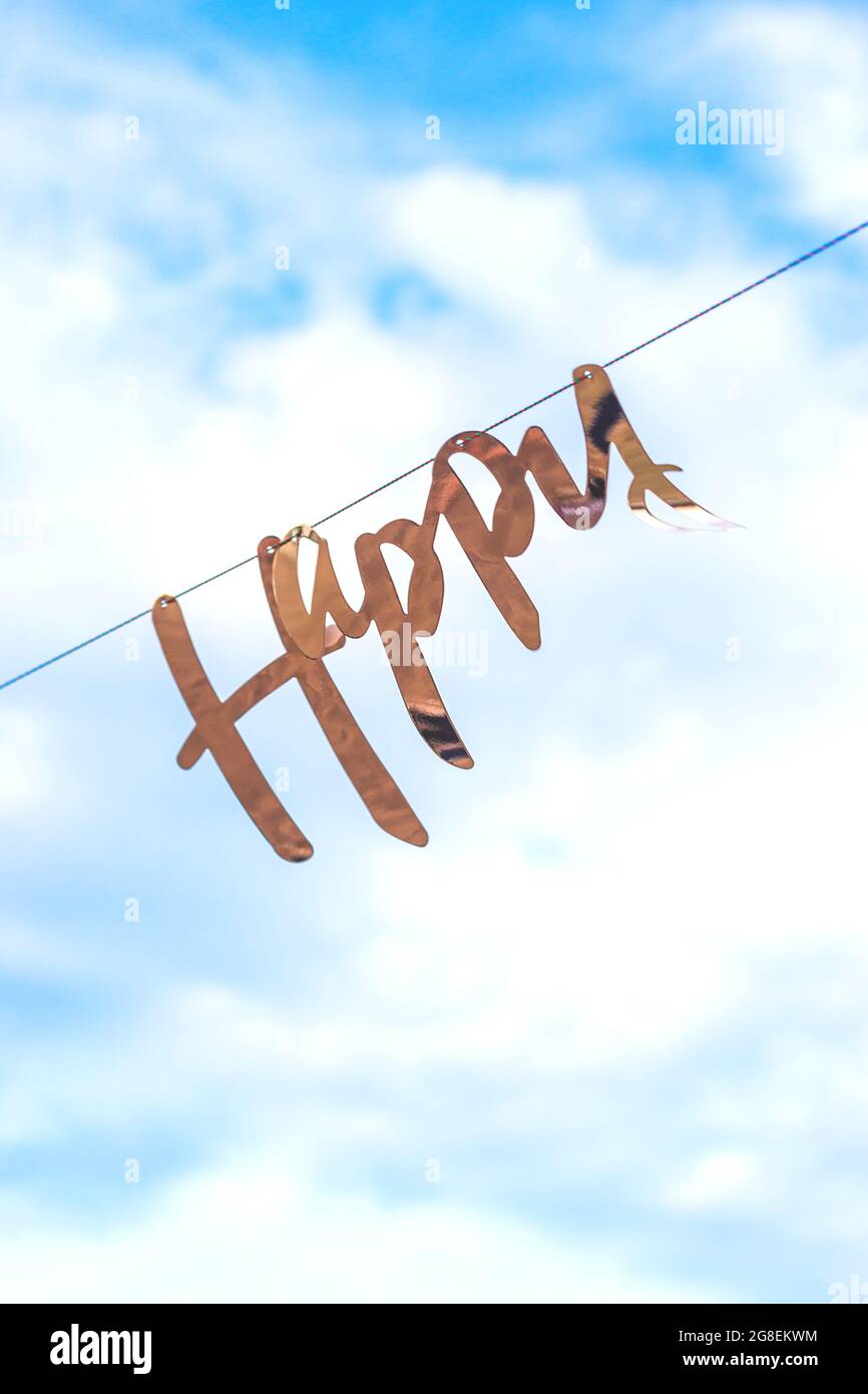 Golden word happy hangs on garland against background of blue sky with ...