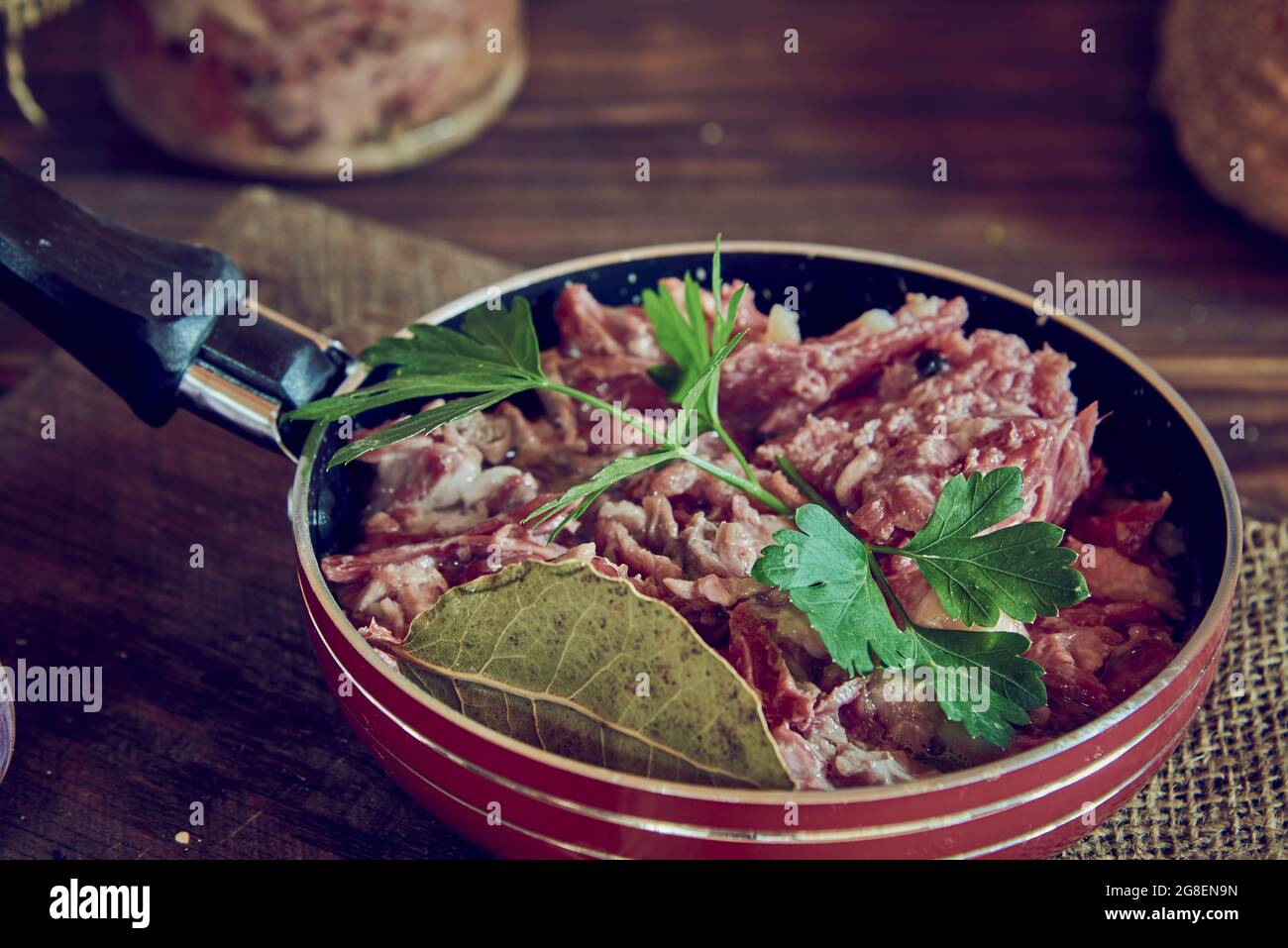 A frying pan with stewed meat seasoned with fresh herbs on a wooden ...