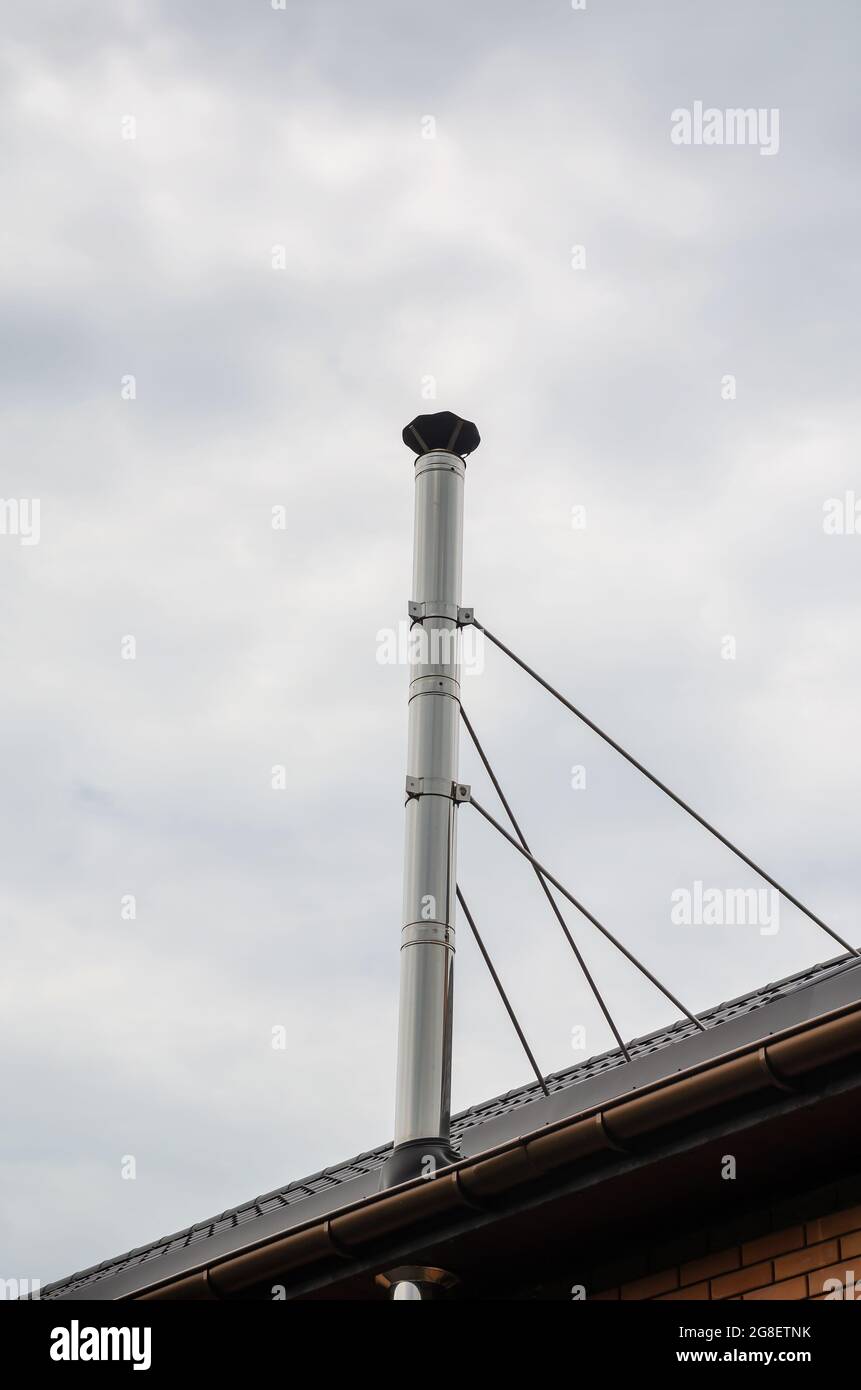 Tall gray metal chimney against an overcast sky. Chimney on the brown ...