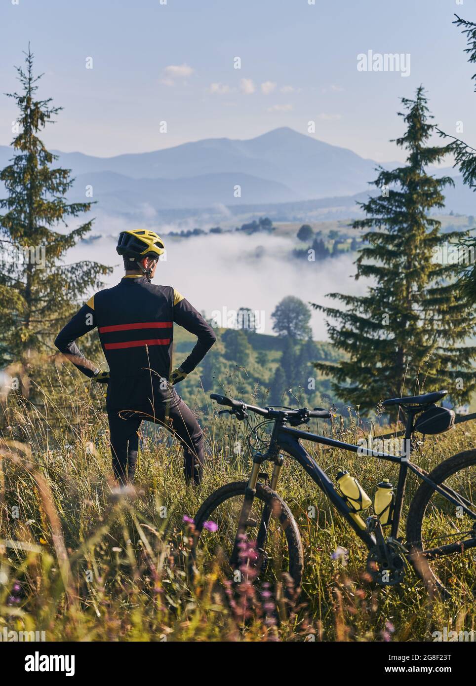 Back view on a cyclist wearing uniform and helmet, standing in grass ...