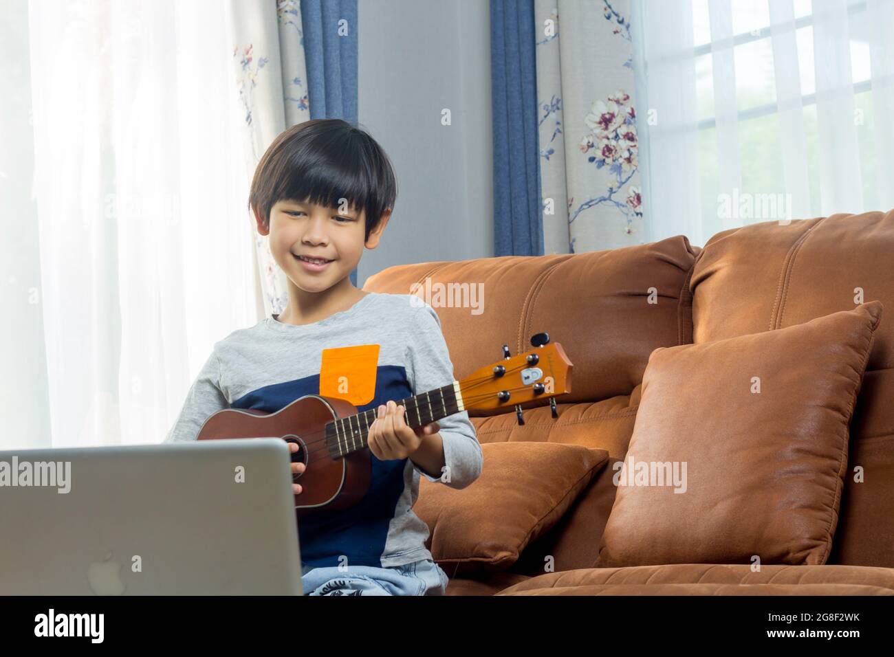 The boy is learning to play the ukulele with online lessons Stock Photo ...