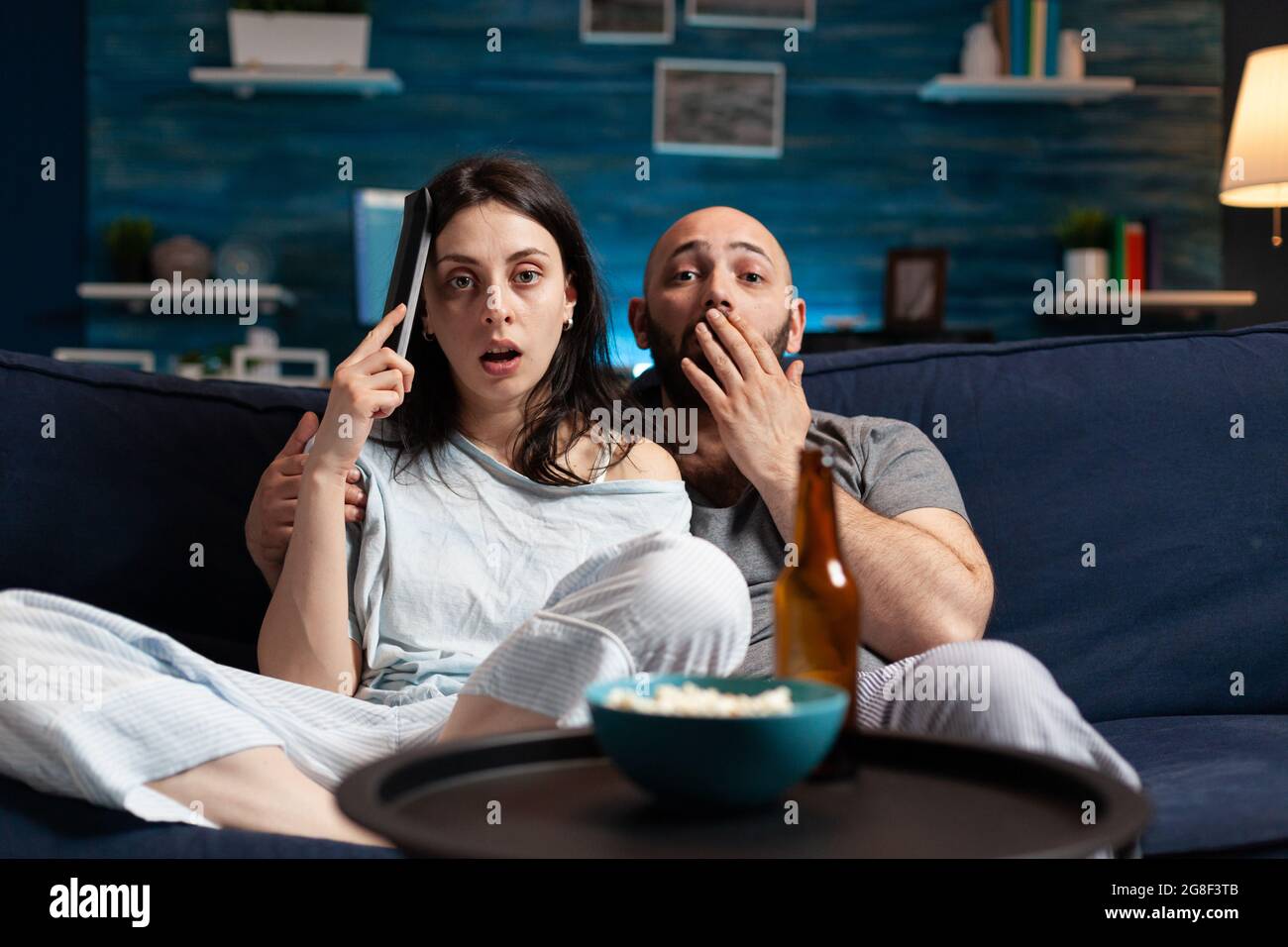 Astonished couple watching movie at night and eating popcorn, drinking ...