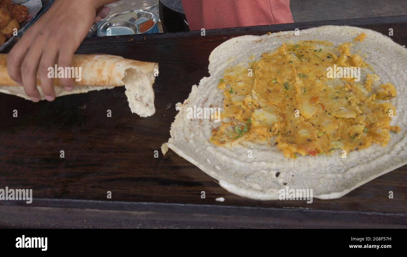 Closeup of a person's hand rolling a delicious Indian Dosa with another ...