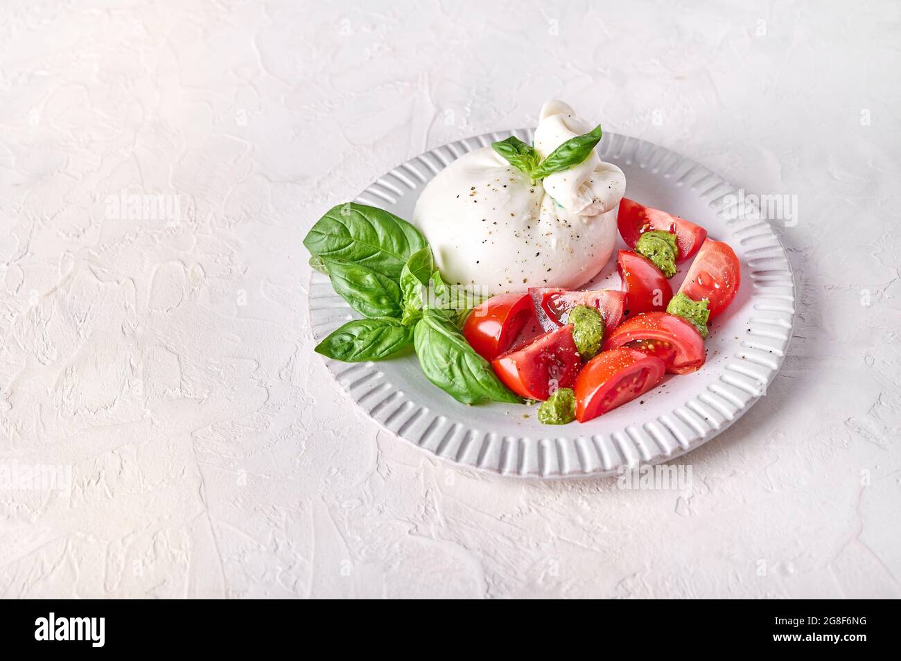 Traditional italian burrata cheese with basil and tomato on light ...