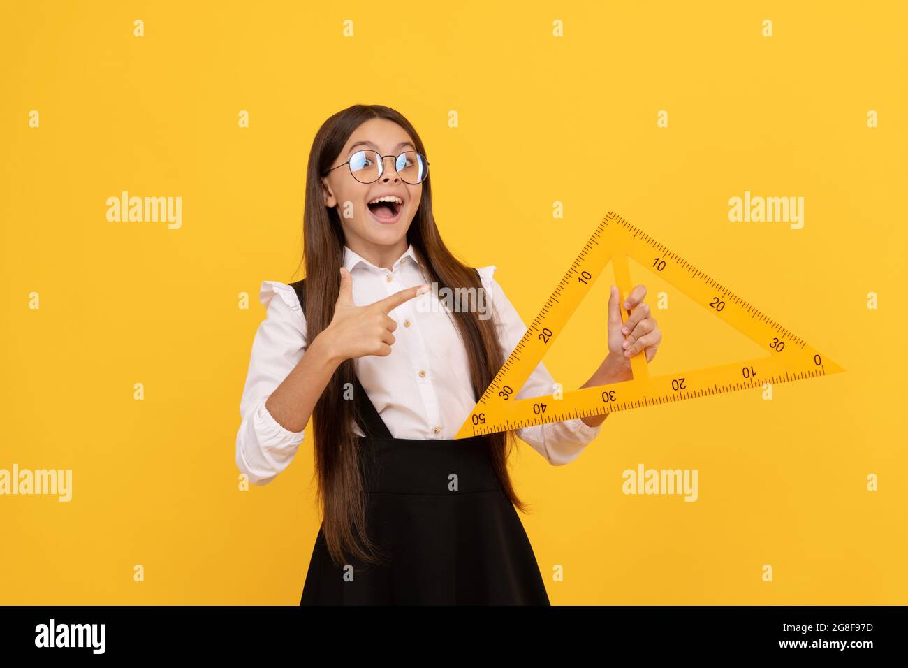 amazed child in school uniform and glasses hold mathematics triangle ...