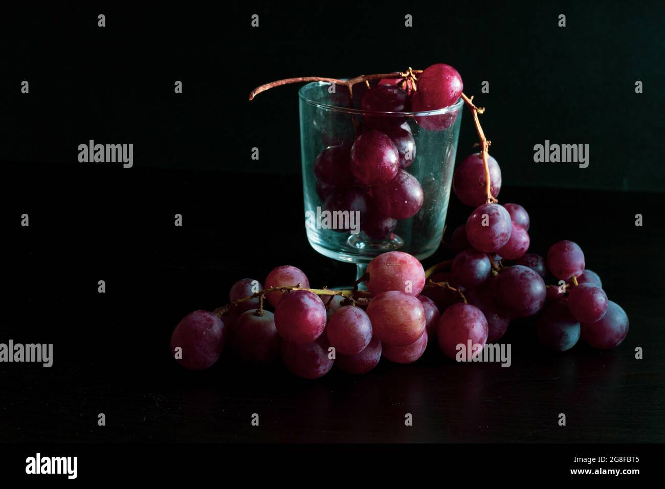 Red grapes in a glass on a black background Stock Photo - Alamy