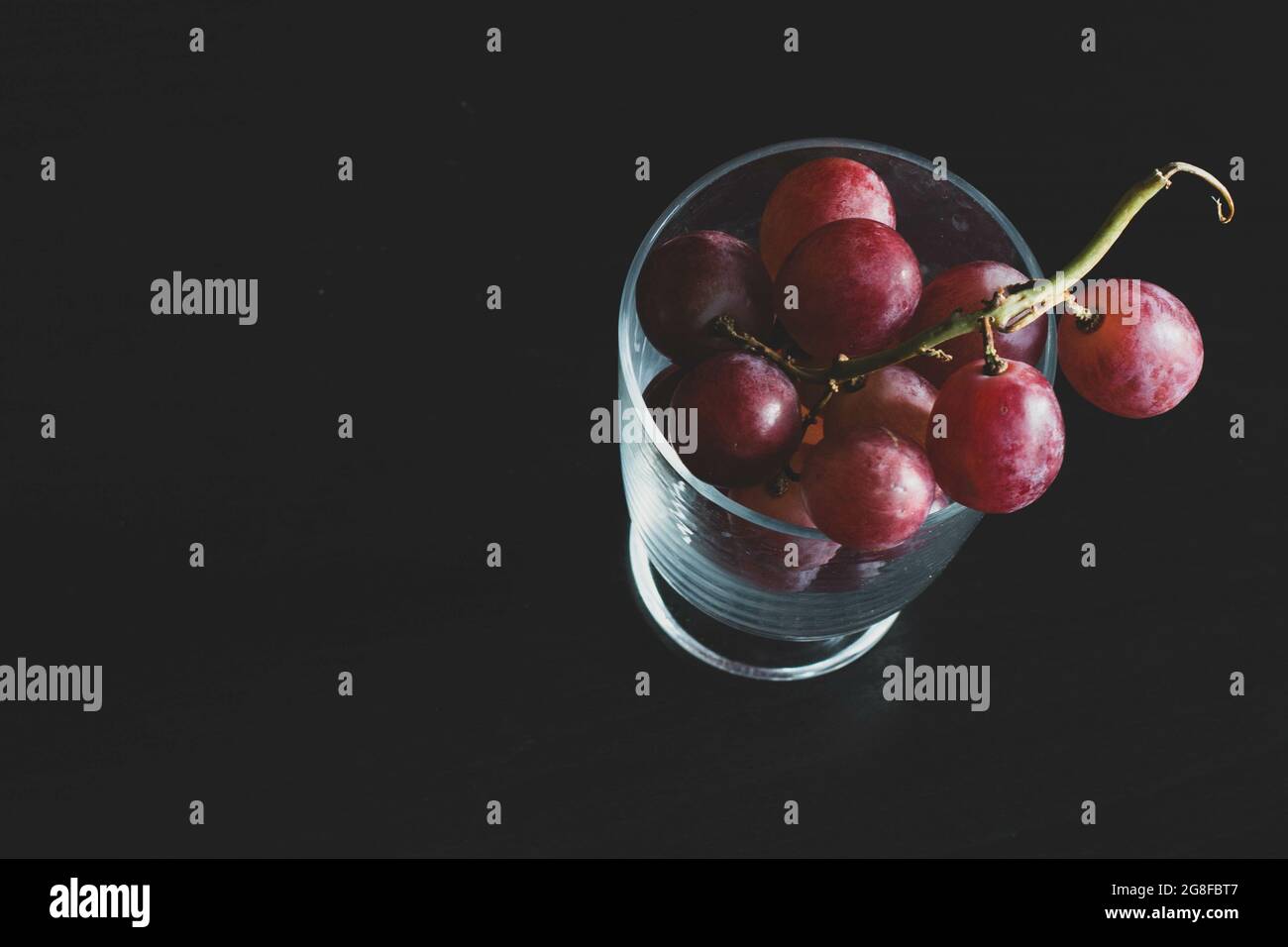 Red grapes in a glass on a black background Stock Photo - Alamy