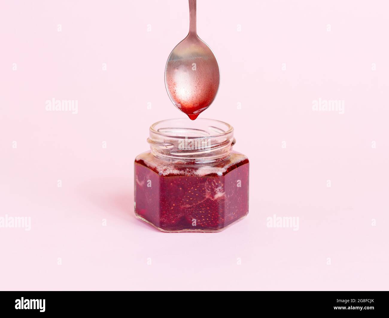 Raspberry jam dripping from a spoon into a small glass jar Stock Photo ...