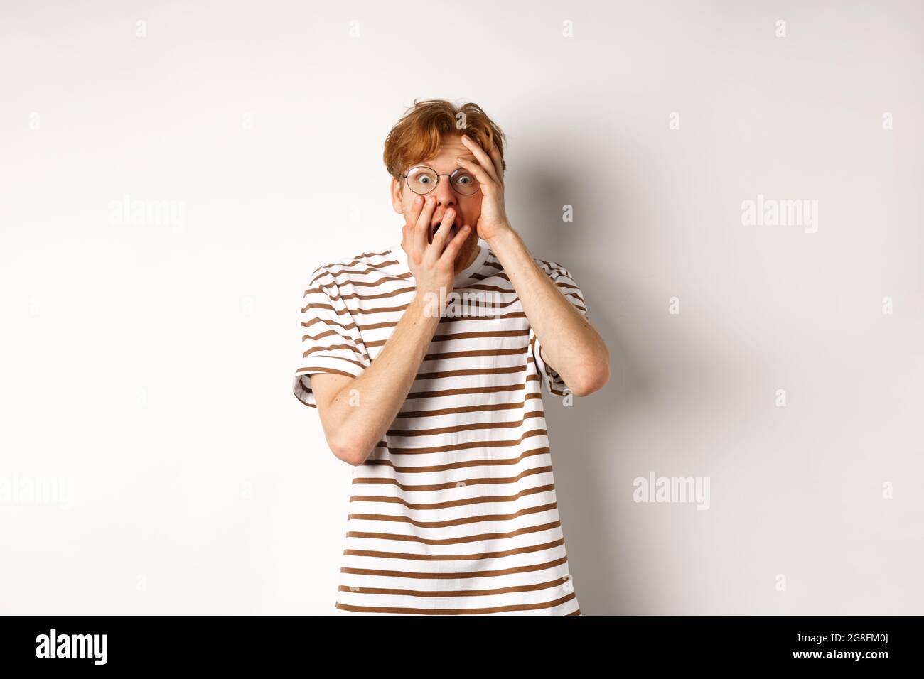 Scared redhead guy screaming terrified, holding hands on face from fear ...