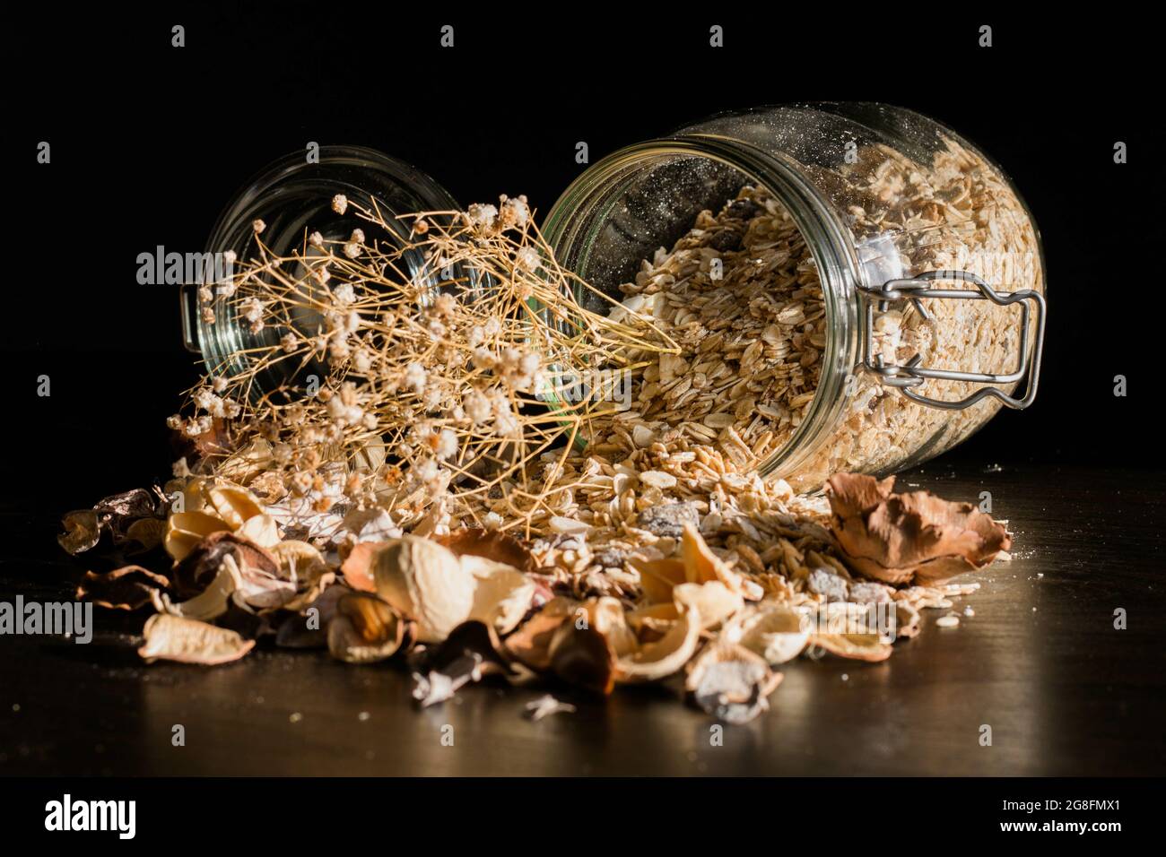 Jar of oat grains fallen on a black background with dry flowers and ...