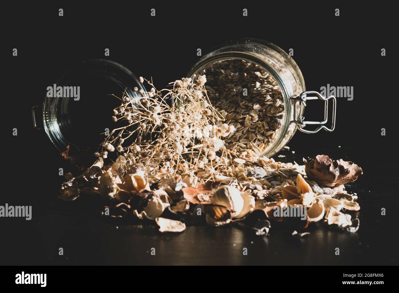 Jar of oat grains fallen on a black background with dry flowers and ...