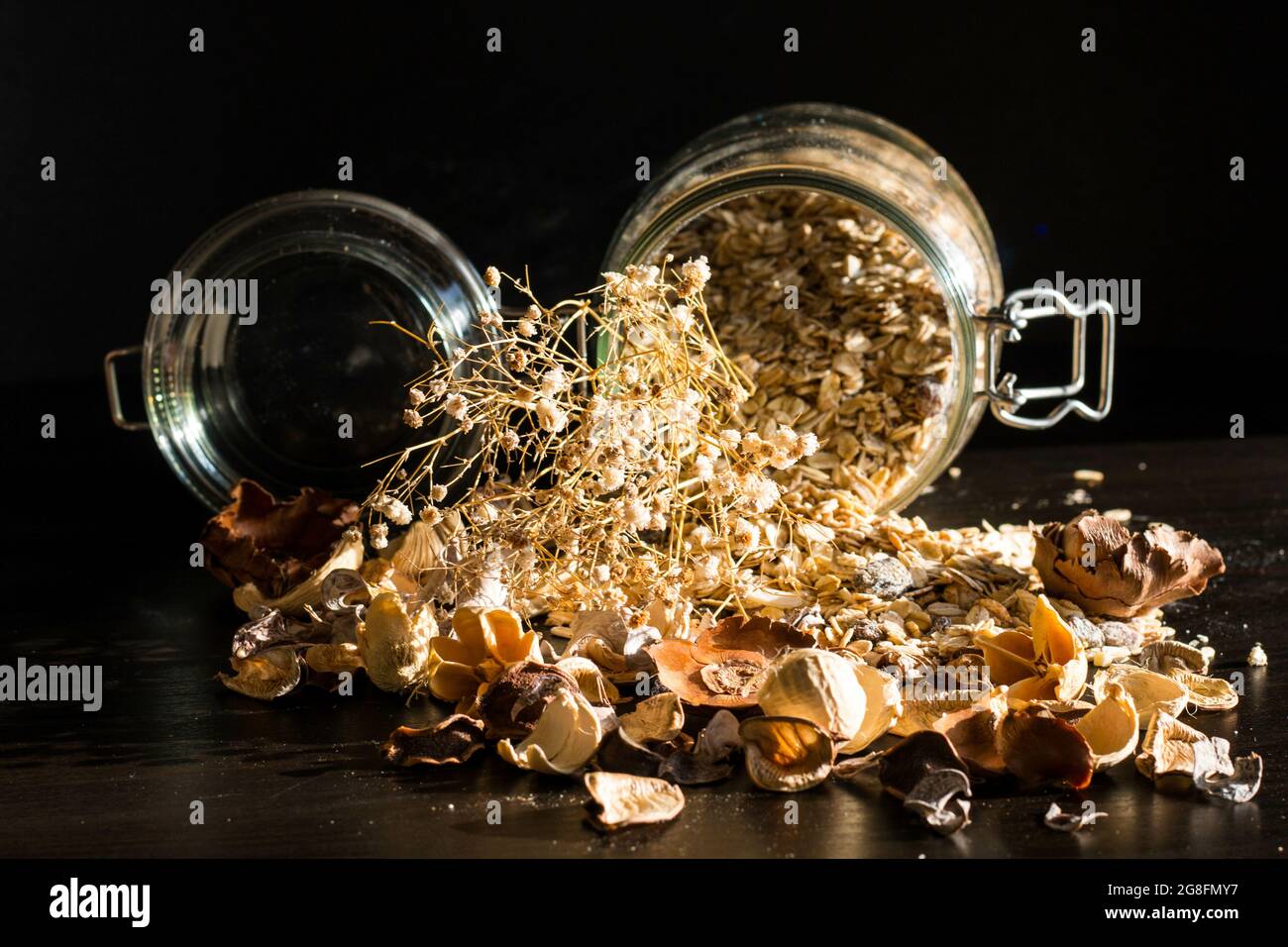 Jar of oat grains fallen on a black background with dry flowers and ...