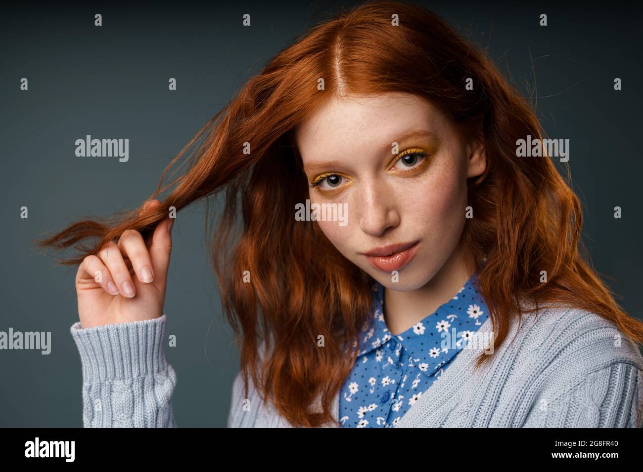 Young Ginger Woman Looking At Camera And Holding Strand Of Her Hair