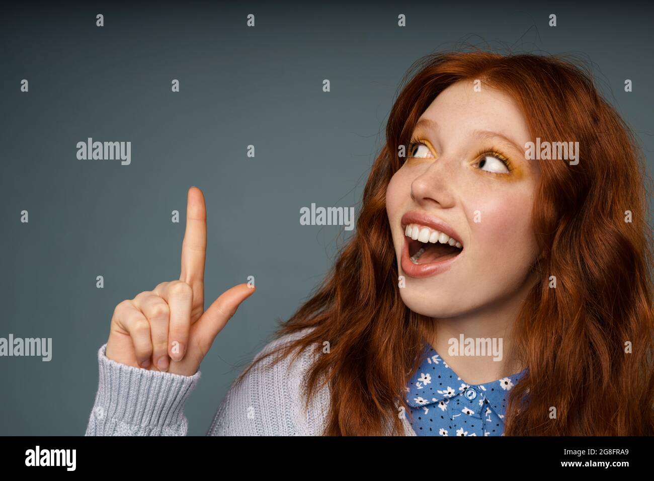 Young ginger excited woman exclaiming and pointing finger upward ...