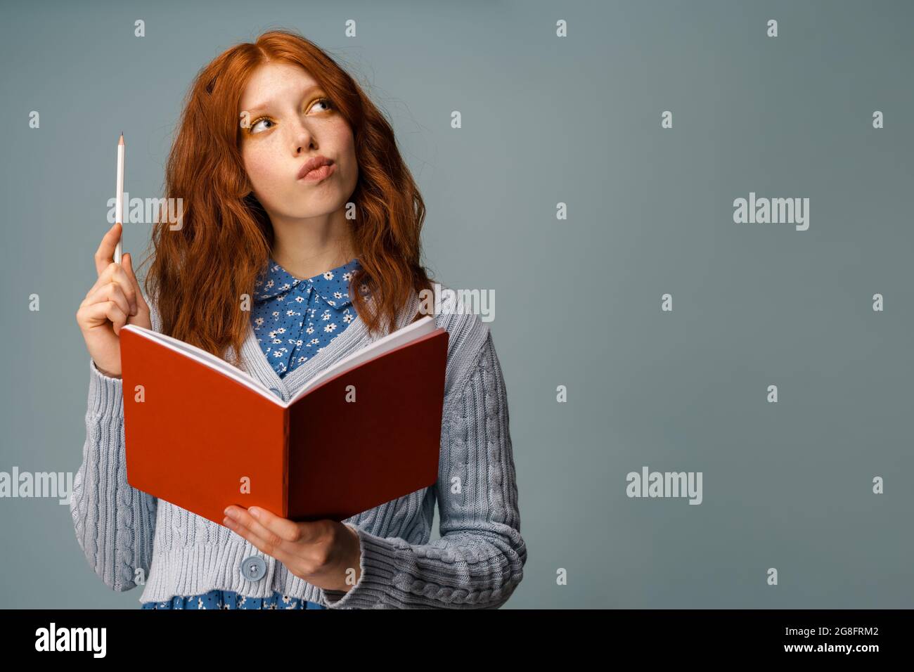 Young ginger thinking woman posing with exercise book and pencil ...