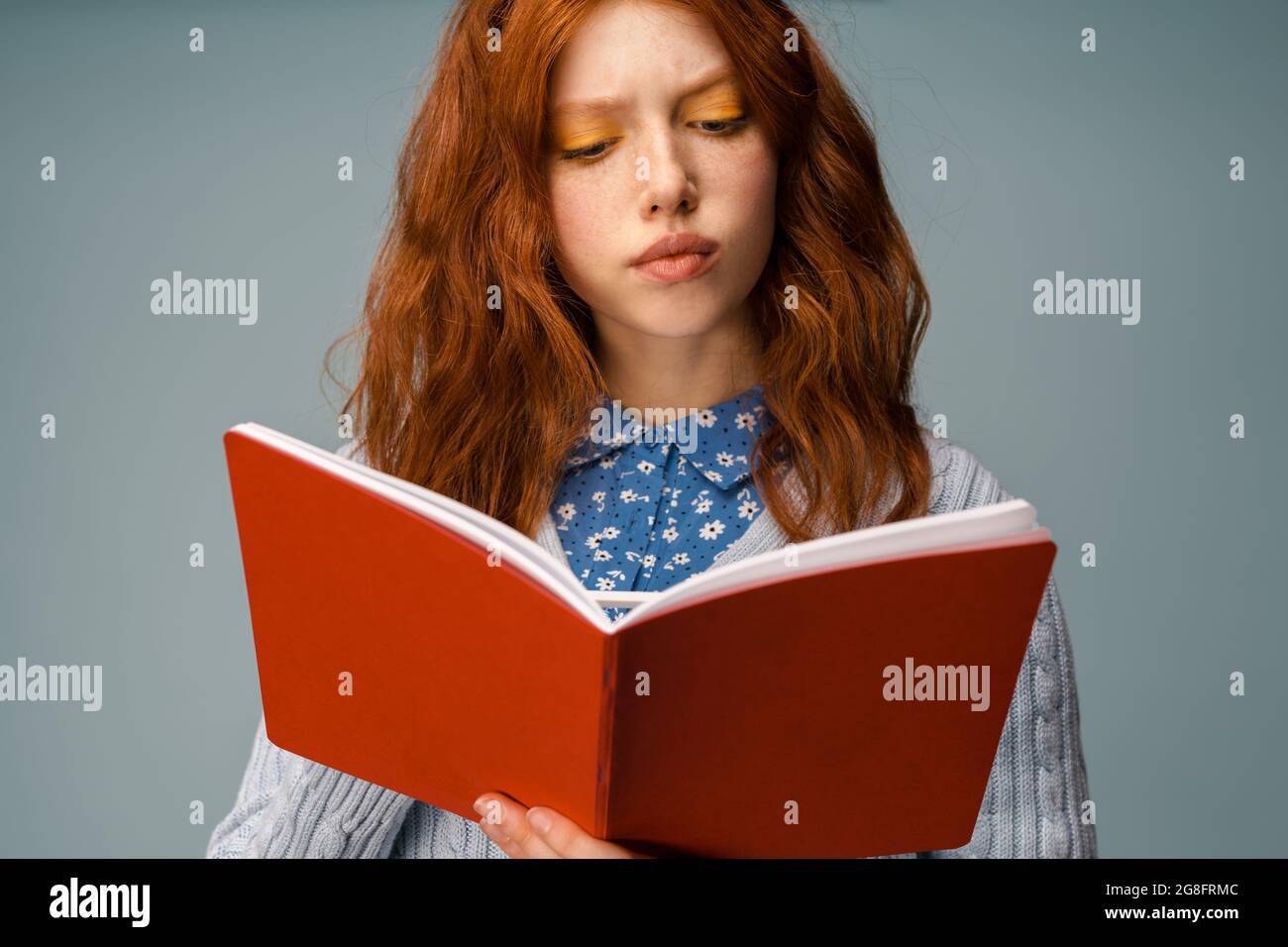 Young ginger puzzled woman posing while reading her diary isolated over ...