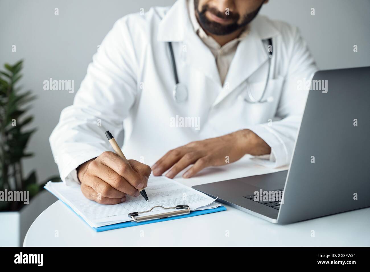 Close up of unrecognizable doctor taking notes sitting at desk front of ...