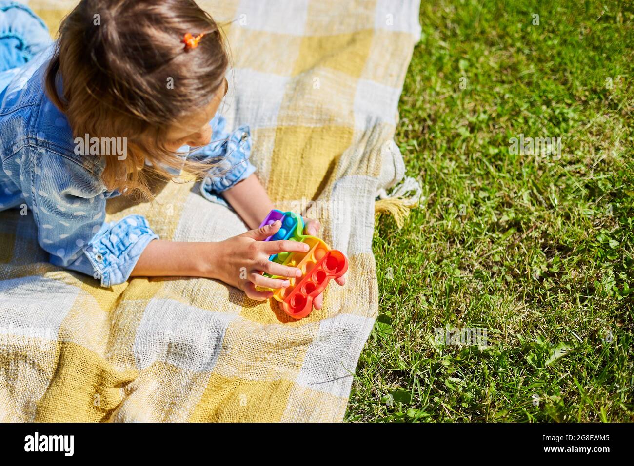 Girl lies on a blanket on grass outdoors and play pop it, kid hands ...