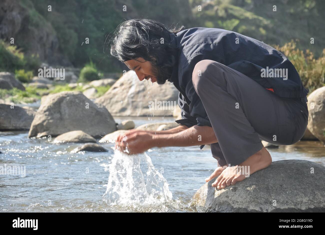 A good looking bearded and long haired young guy washing his face in ...