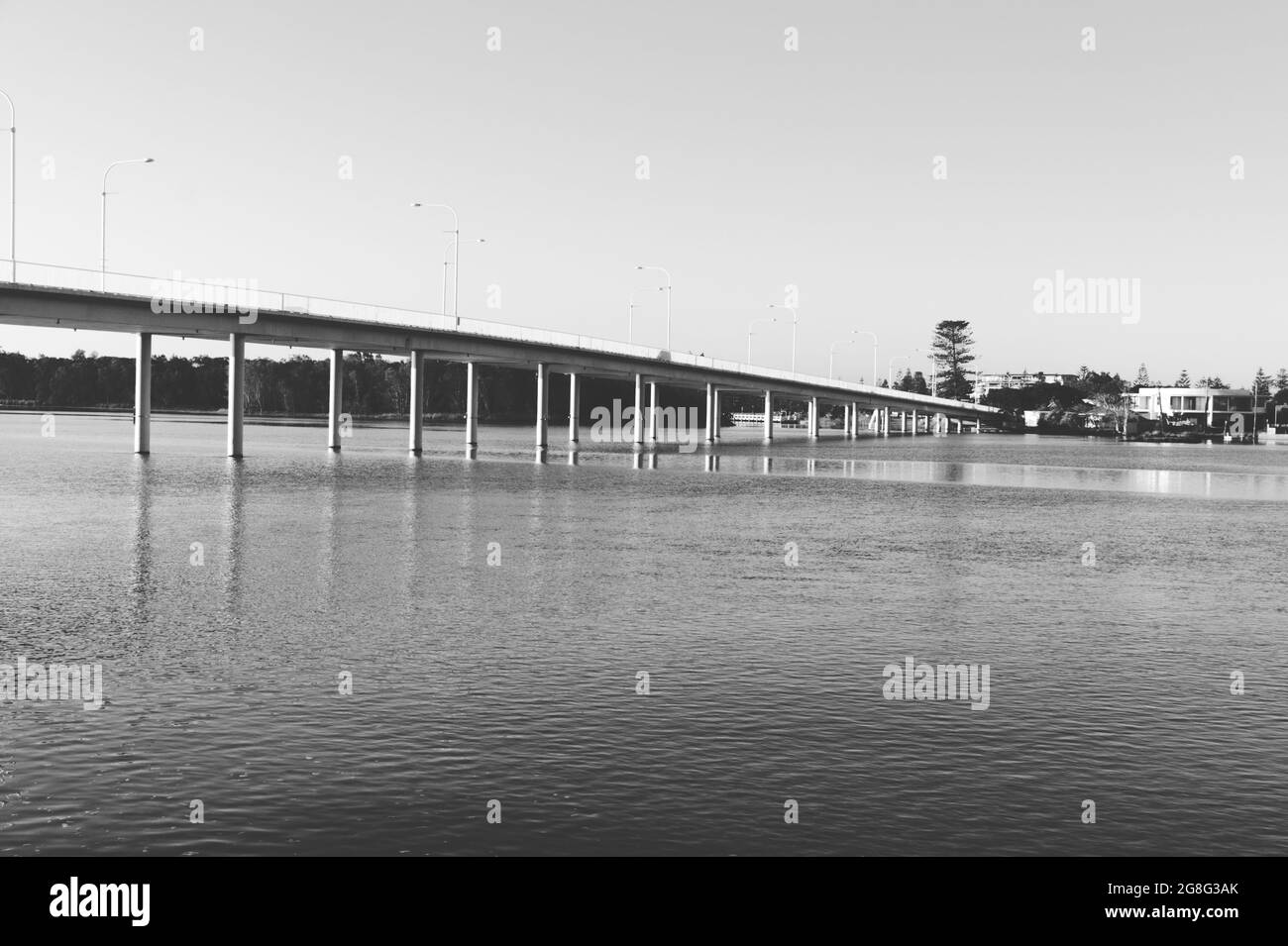 Greyscale shot of a bridge above a wide river leading to some buildings ...