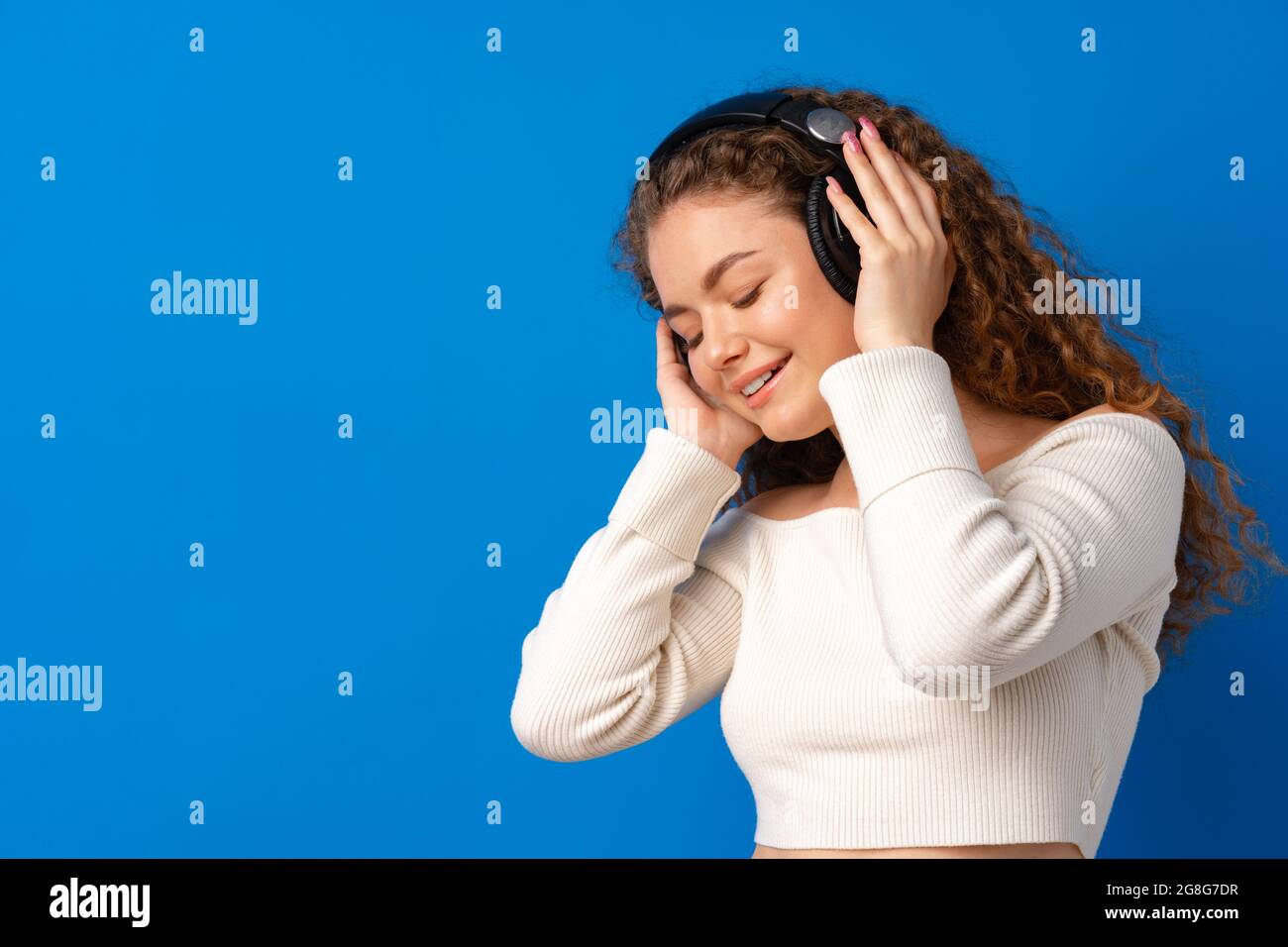 Young attractive curly woman listening to music with headphones against ...