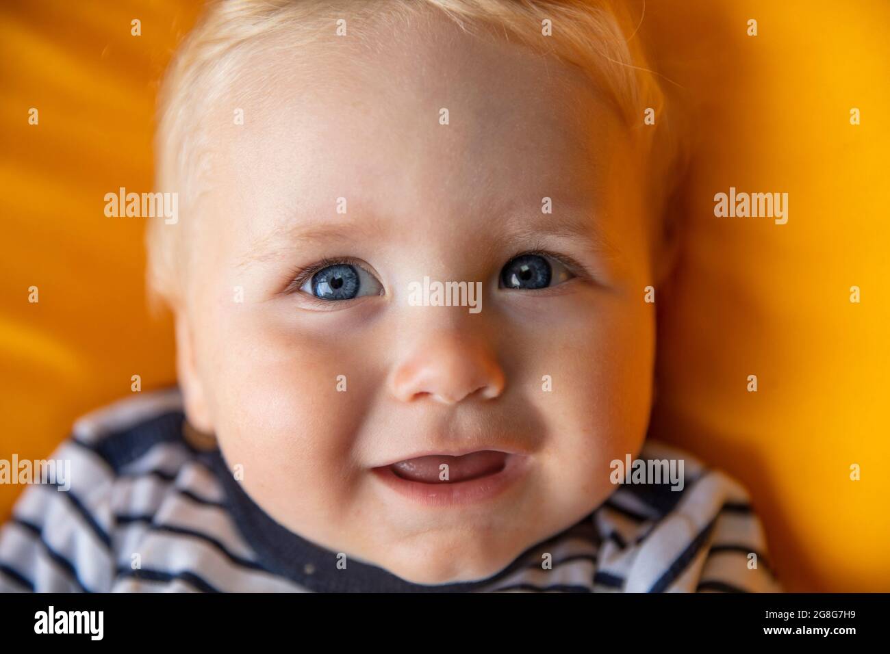 Close up of a cute 9 month old baby boy with blue eyes on a yellow ...