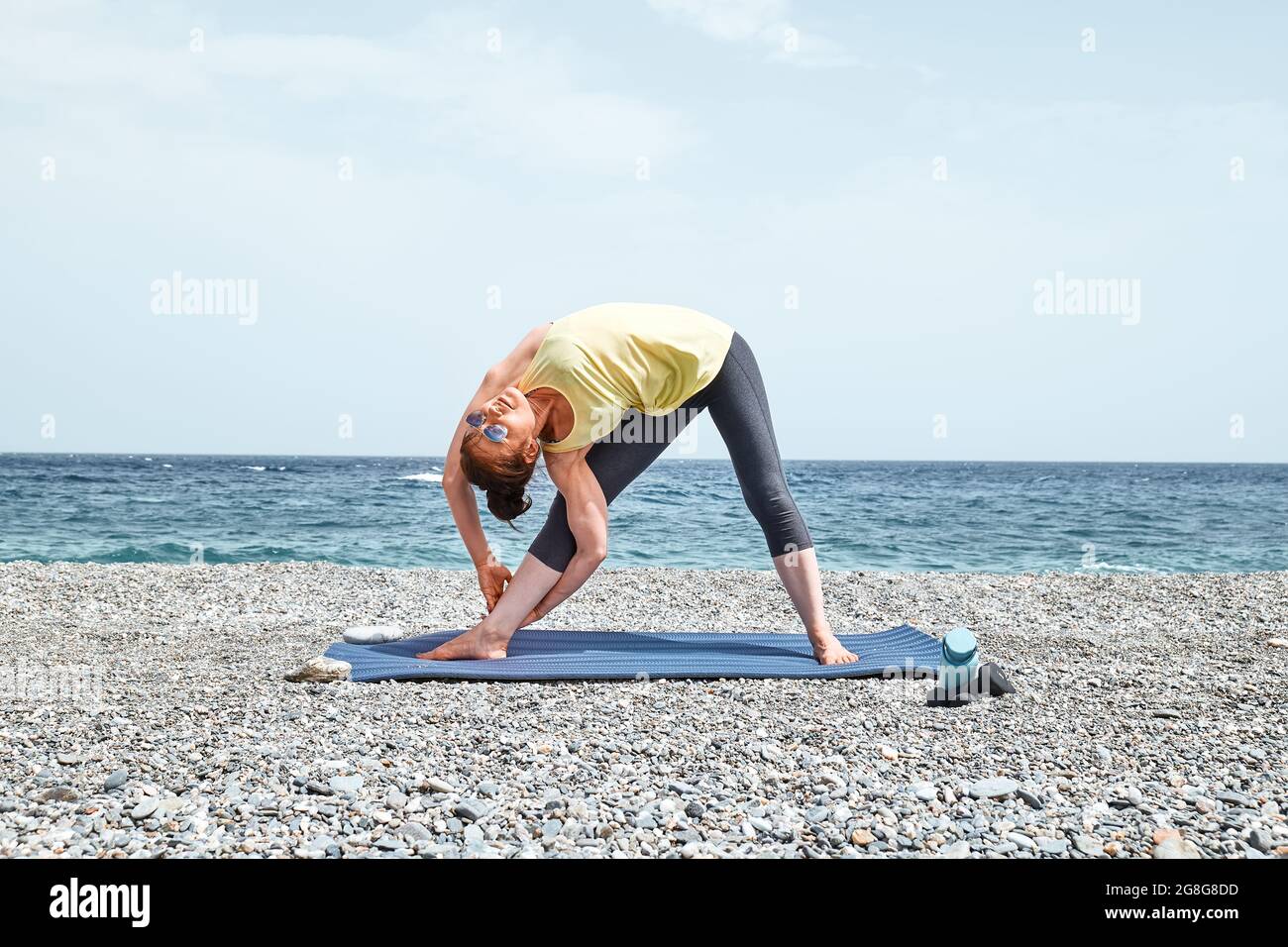Slim Woman doing yoga stretch pose on the beach with blue sea in ...