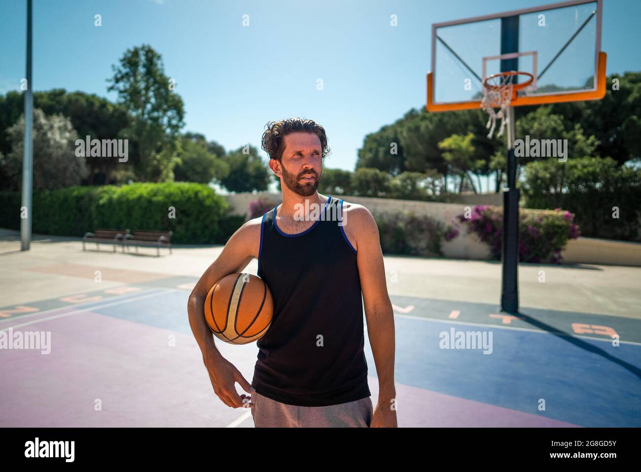 Handsome tired basketball player standing on basketball court outdoors ...