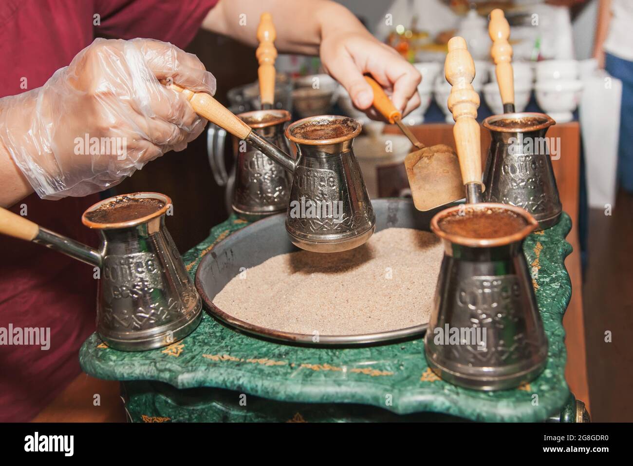 Woman makes turkish coffee on a coffee machine with sand in cezve ...