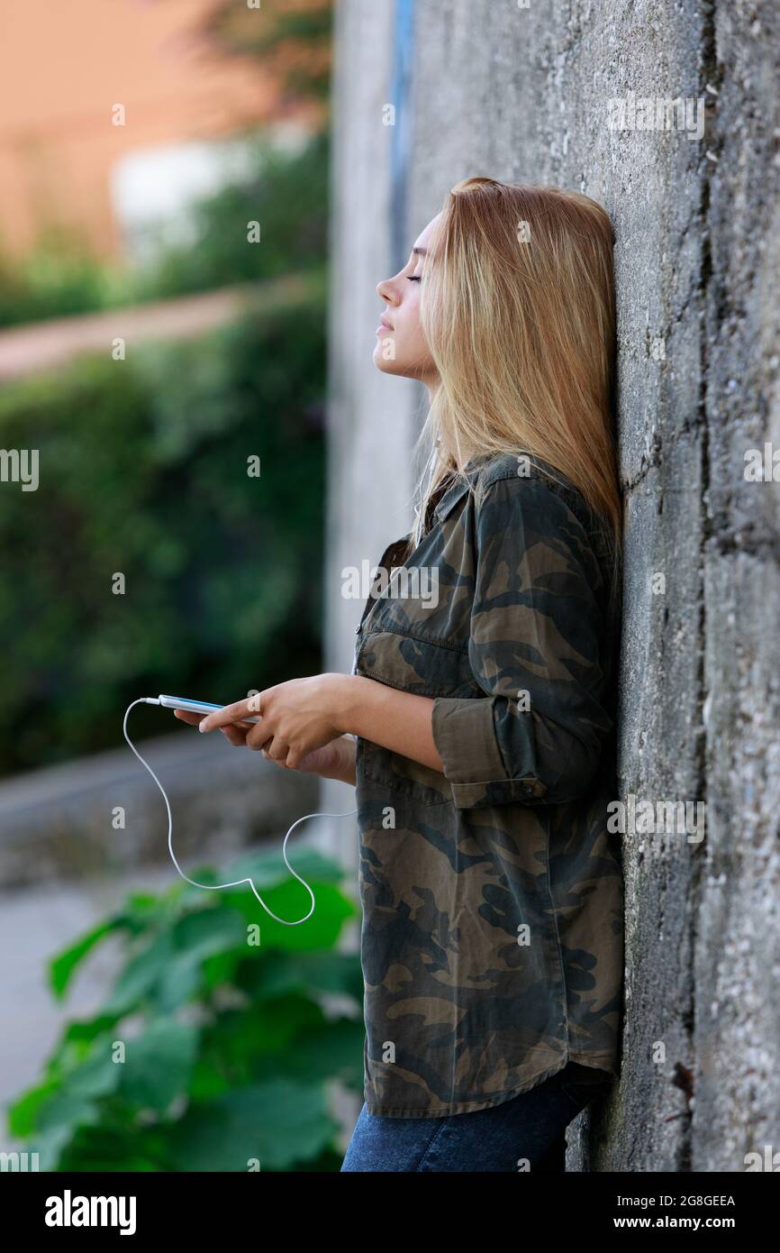 beautiful girl leaning against a concrete wall in a suburban area, she ...