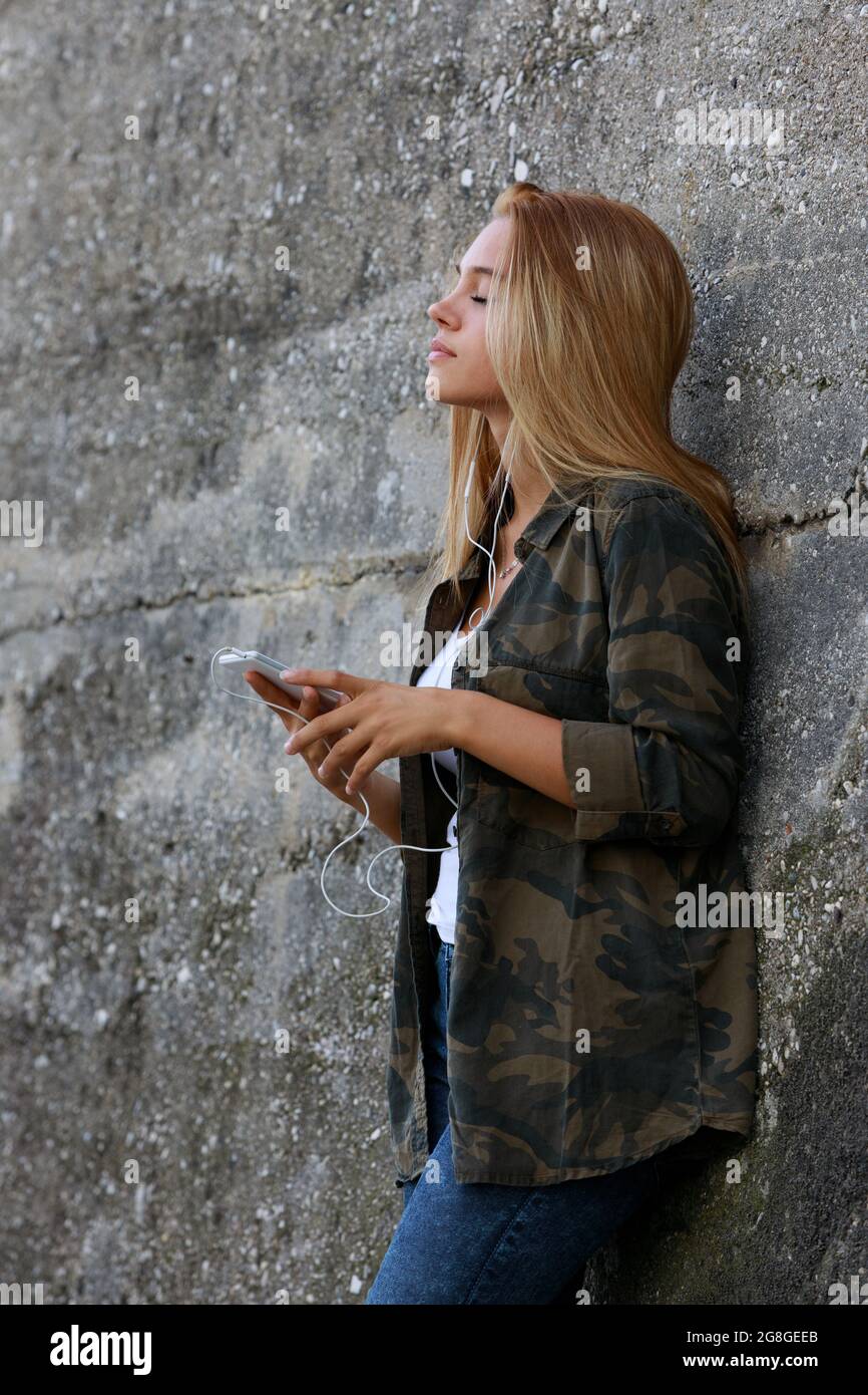 beautiful girl leaning against a concrete wall in a suburban area, she ...