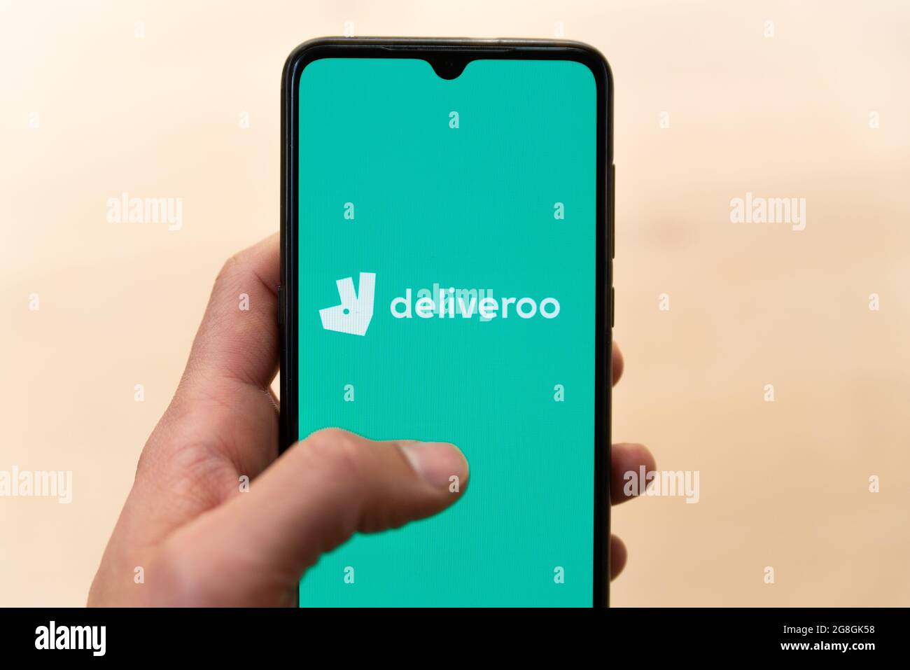 A hand holds a mobile phone with the Deliveroo logo visible on the ...